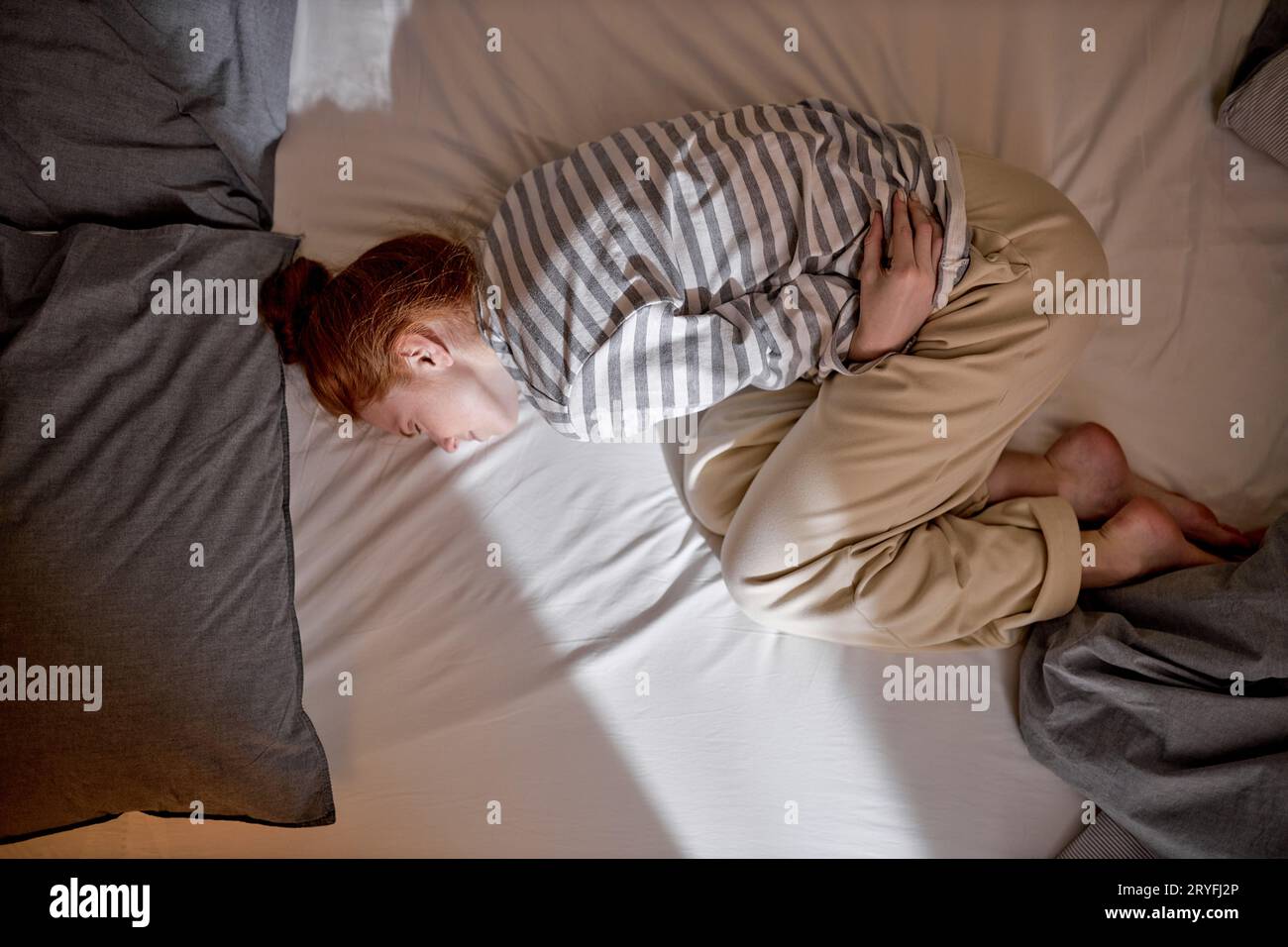 Top view of sick young ginger redhead woman lying in bed touch belly ...