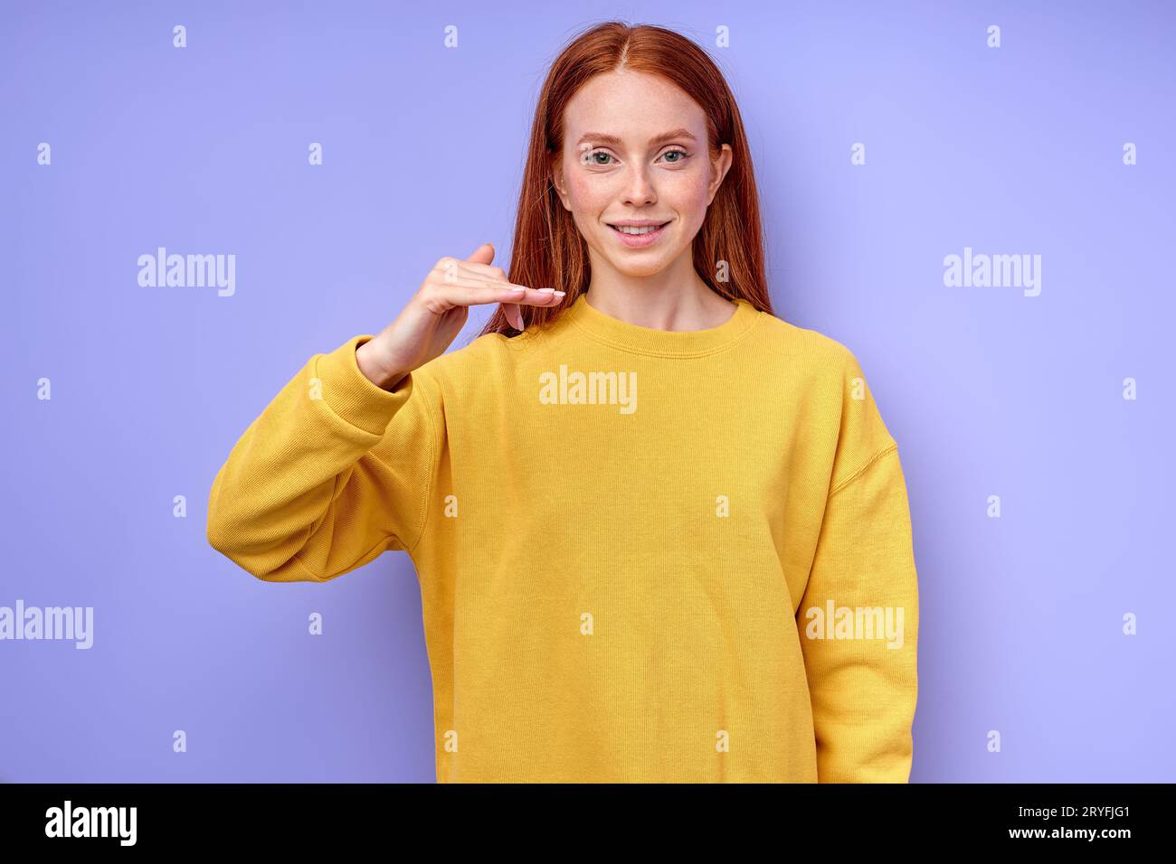 cheerful Caucasian woman with long red hair demonstrating the letter F ...