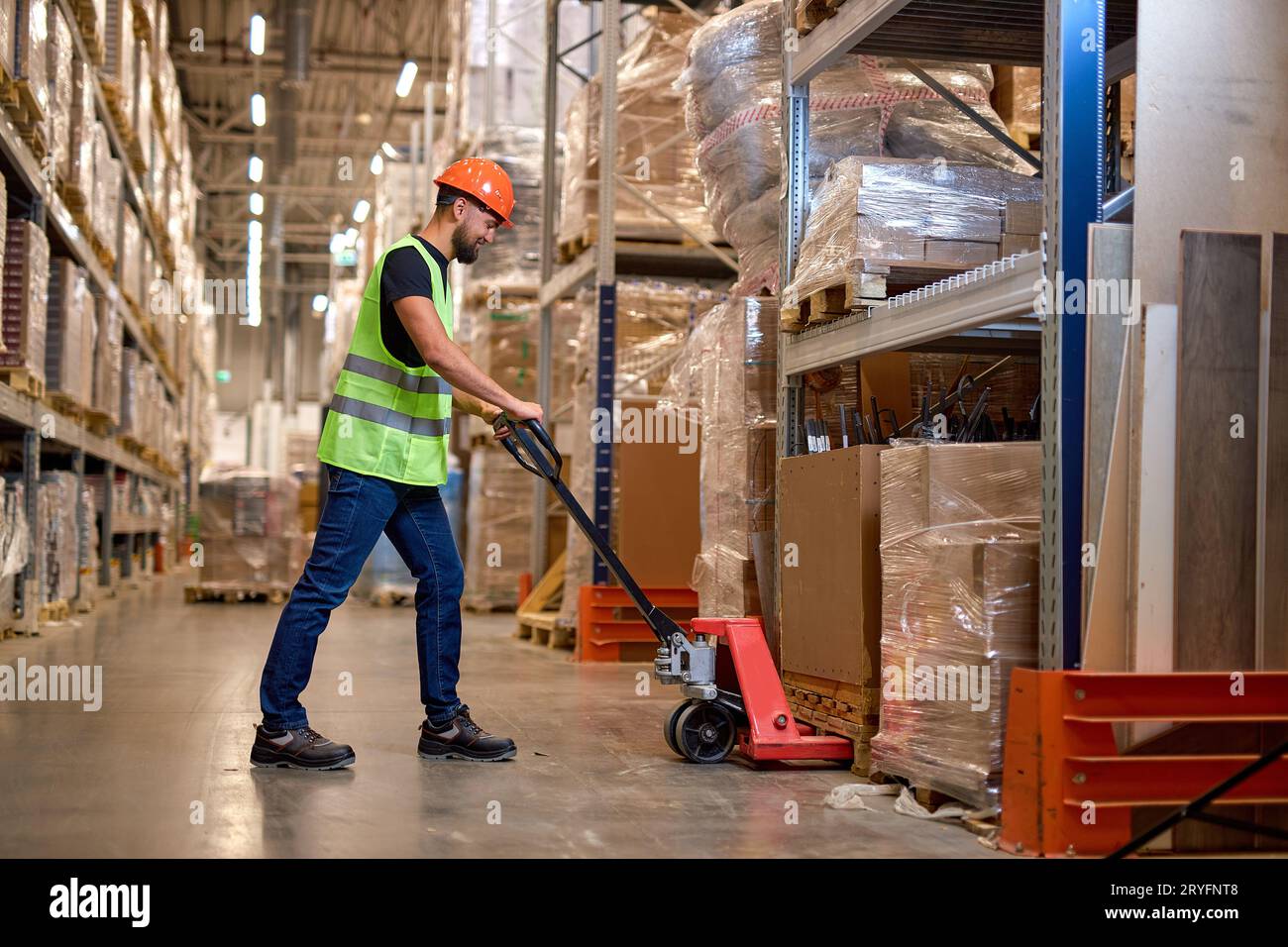 male staff worker in warehouse uses hand pallet stacker to transport ...