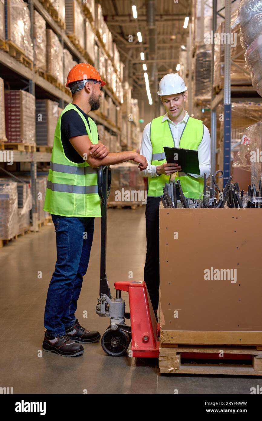 two men warehouse workers with hand pallet jack lift stand having talk ...