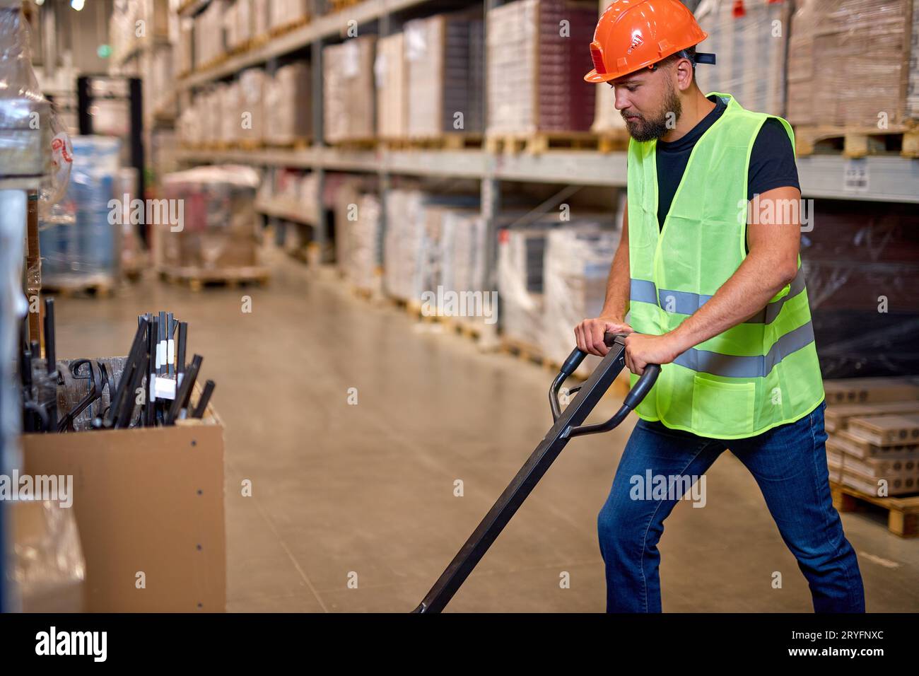 male staff worker in warehouse uses hand pallet stacker to transport ...
