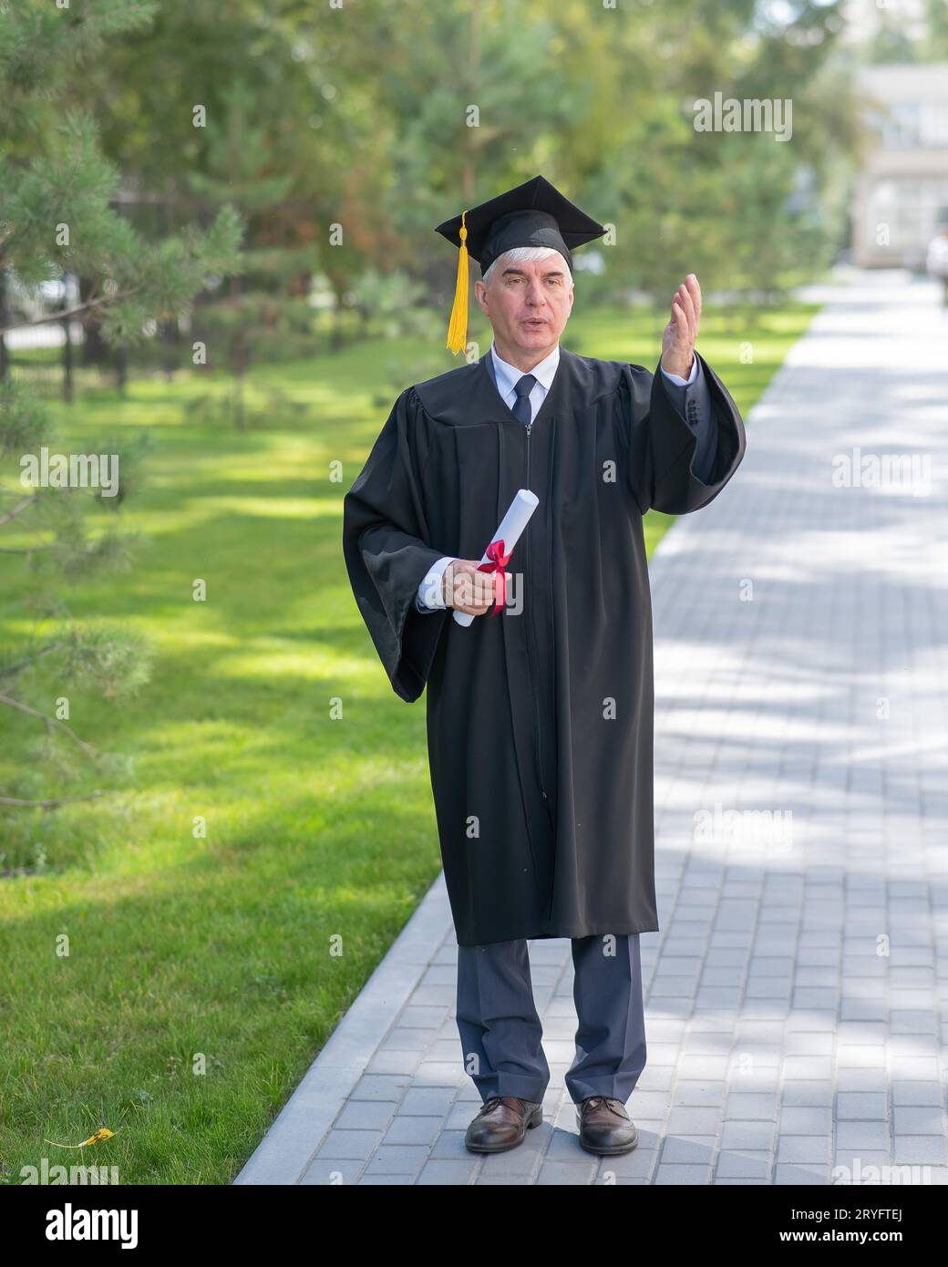 Serious old man in graduation gown holding diploma outdoors Stock Photo ...