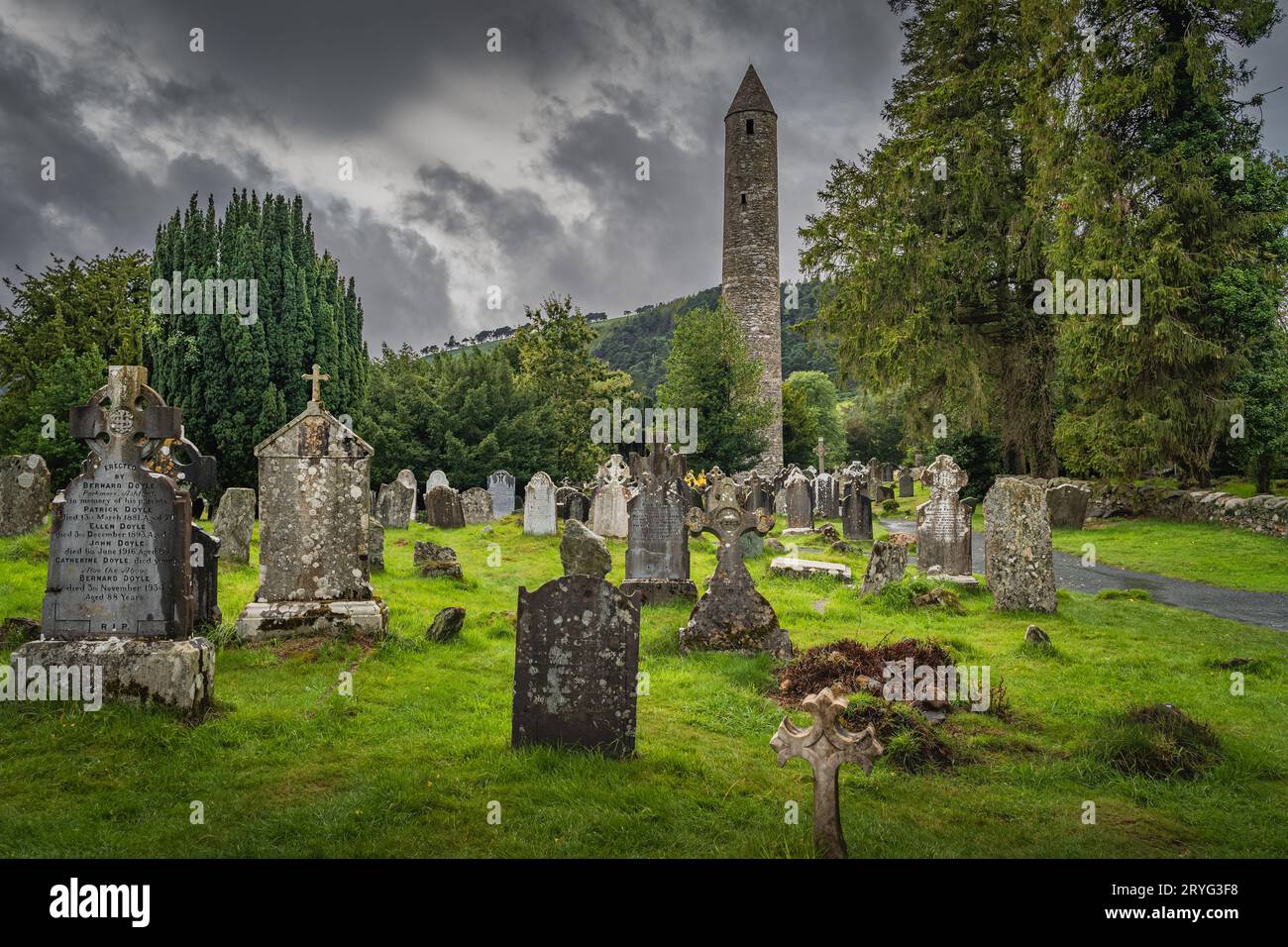 Medieval tower and ancient graves with Celtic crosses in Glendalough ...