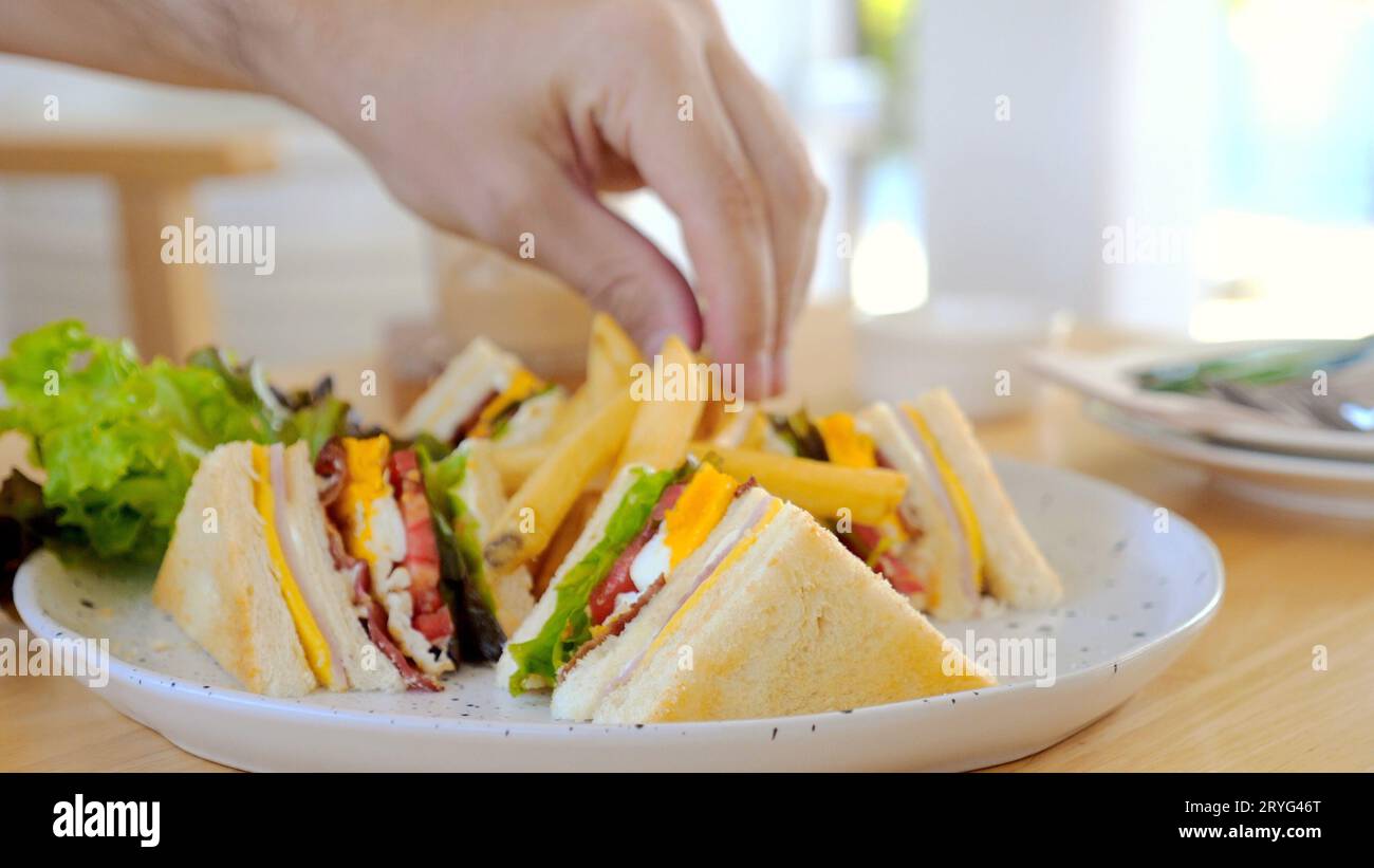 Man hand take a crispy French fries from plate with club sandwich Stock ...