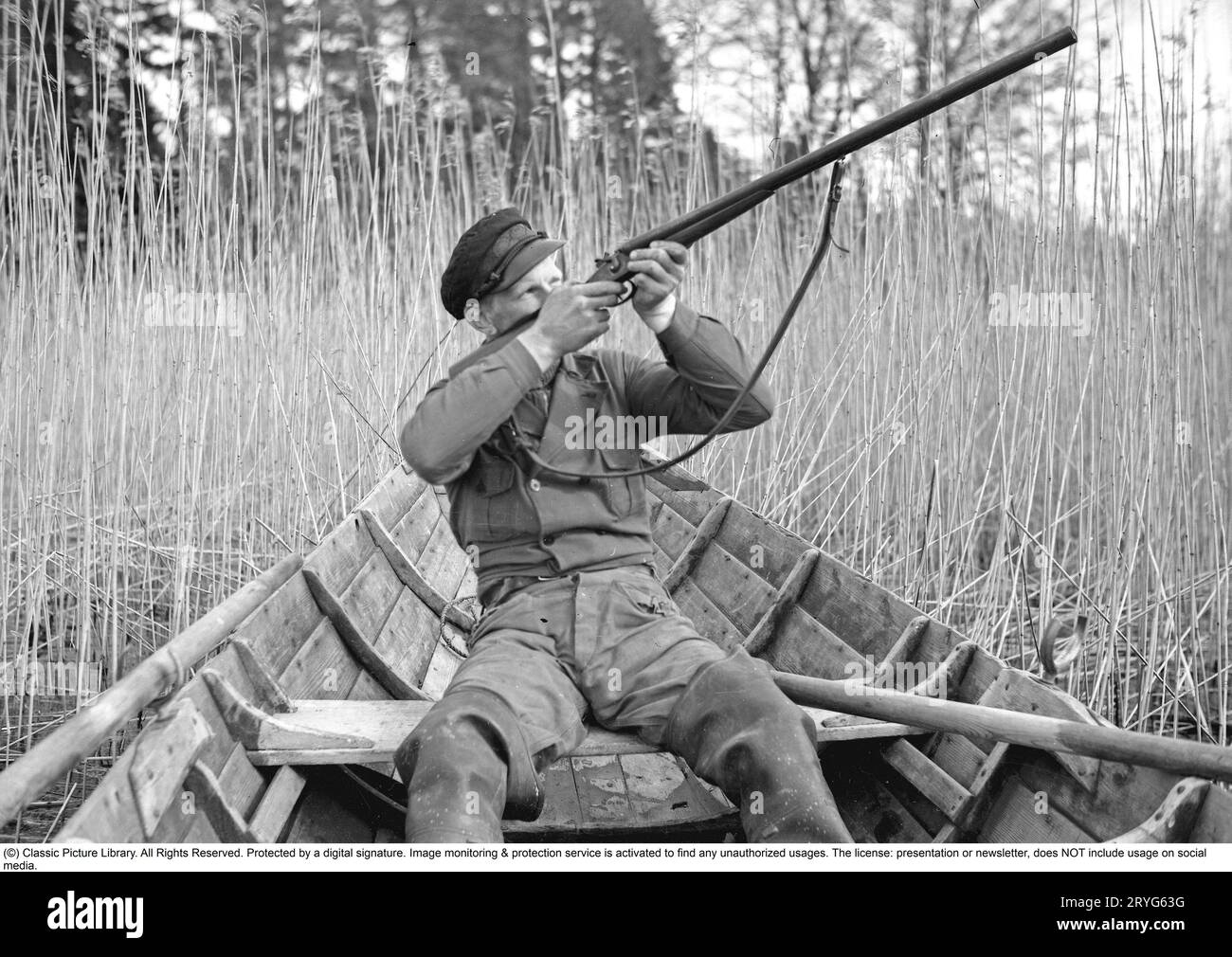 In the 1930s. A man sits in a rowing boat and aims his rifle upwards to ...