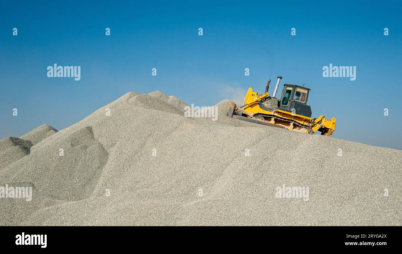 A heavy bulldozer on a mountain of gravel loading under blue sky Stock ...