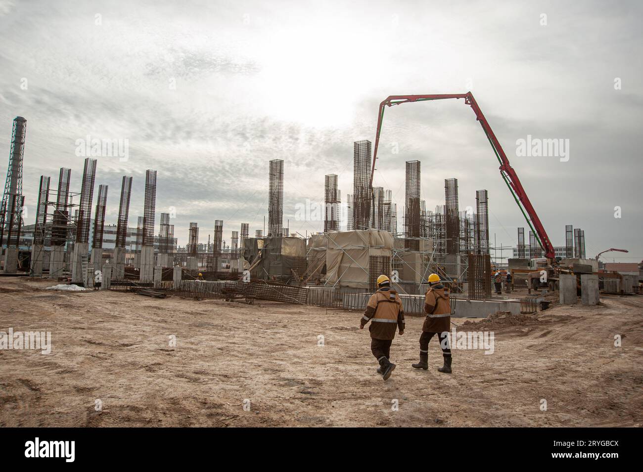 Two workers in special equipment and yellow helmets with factory construction in the background ...