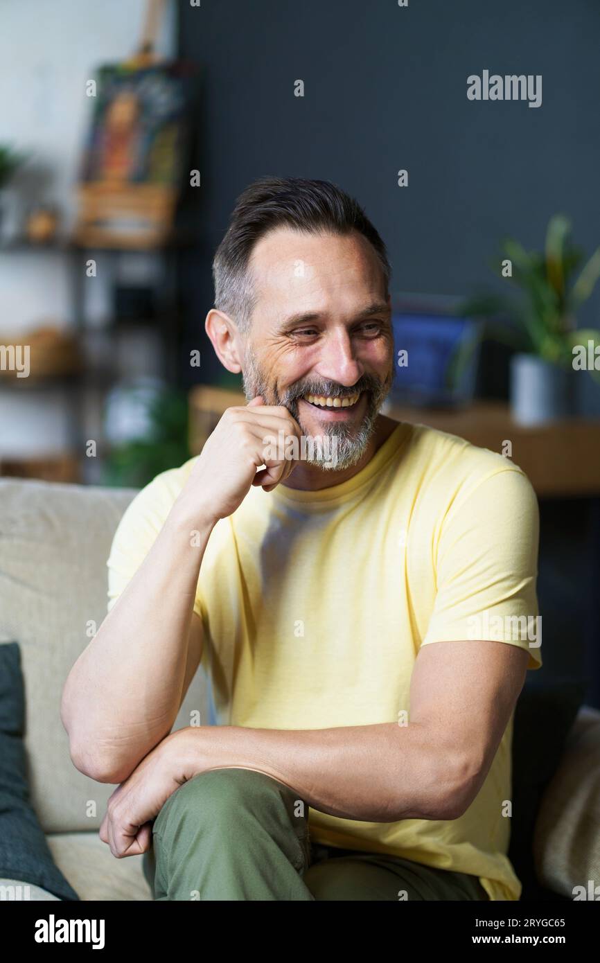 Cheerful handsome middle aged freelancer man sitting on the sofa with a ...