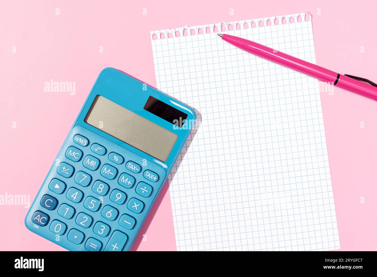 Flat lay of a calculator, blank grid paper notebook and pen on pink ...