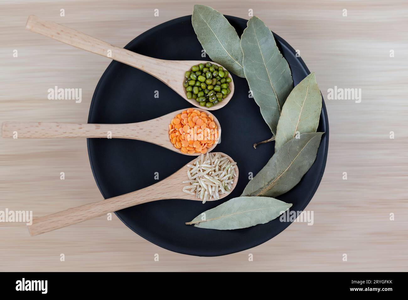 Rice, moong beans and dal in wooden spoons next to star anise seeds ...