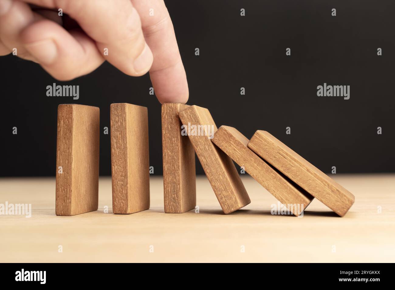 Hand Stopping Falling wooden Dominoes effect Stock Photo - Alamy