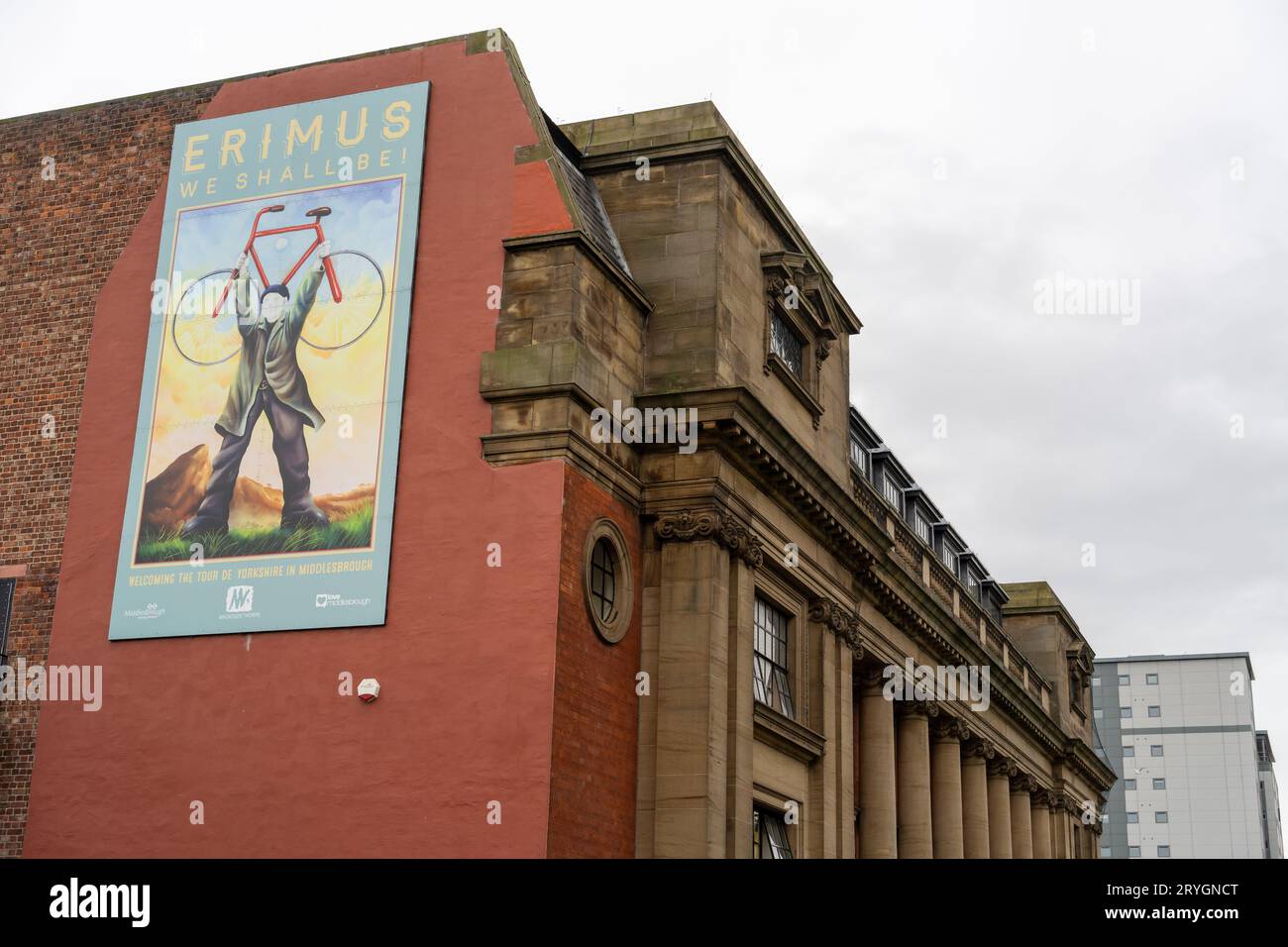A sign or artwork on the side of the library reads, 'Erimus - We Shall ...