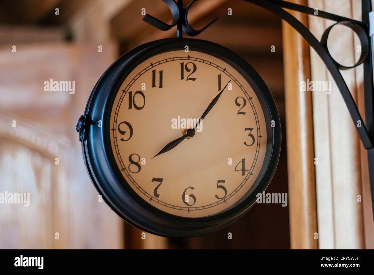 Round vintage clock in black metal hanging on corner mount on wooden ...