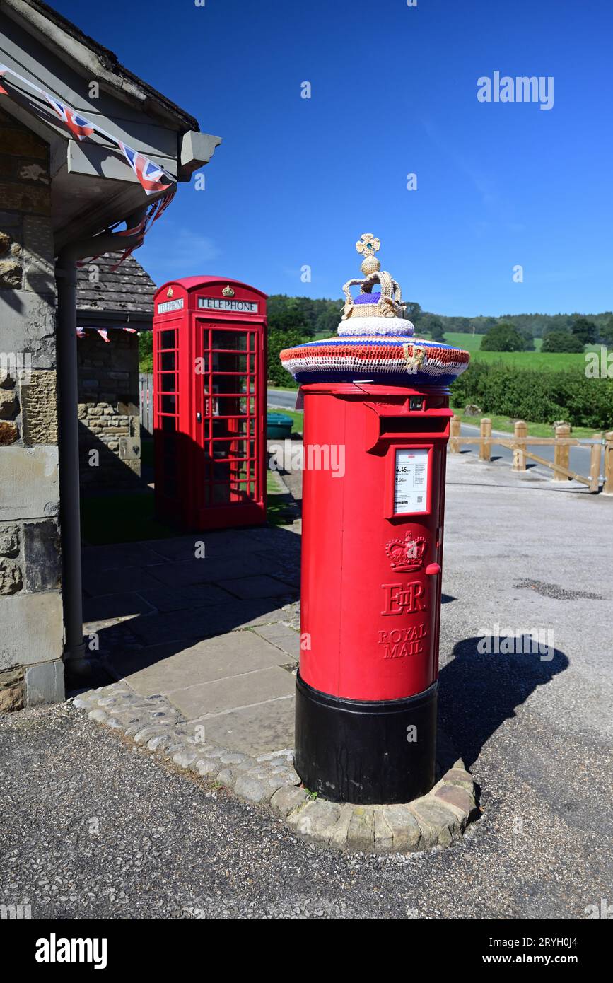 A free-standing letter box with a knitted top, beside a red telephone ...