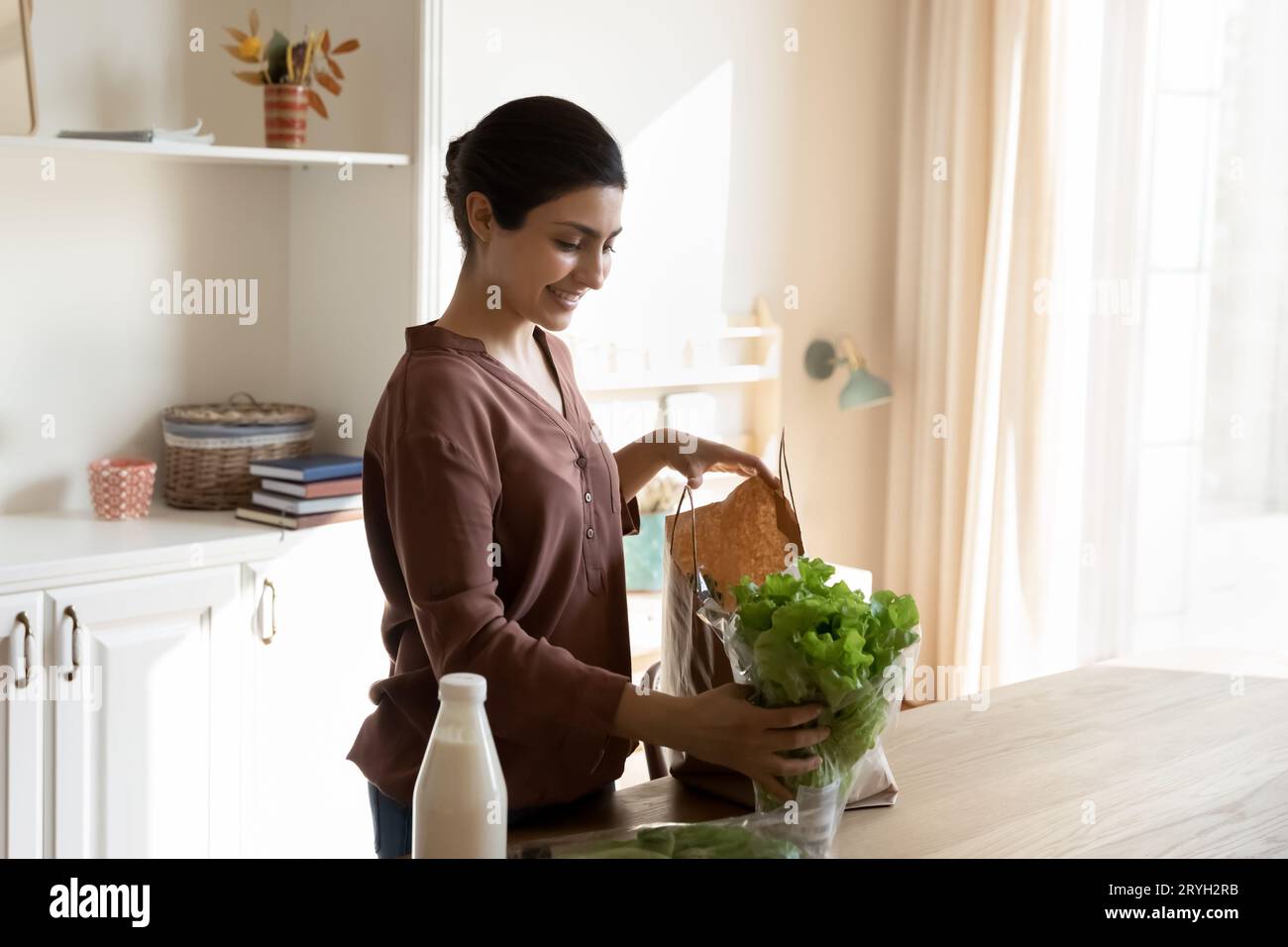 Smiling Indian woman unpacking paper bag with products in kitchen Stock ...