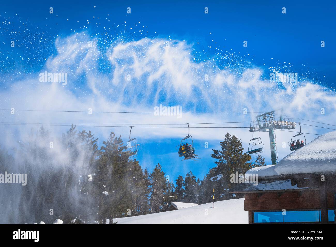 Snow cannon spreading snow on a ski slope. Skiers riding up on chair ...