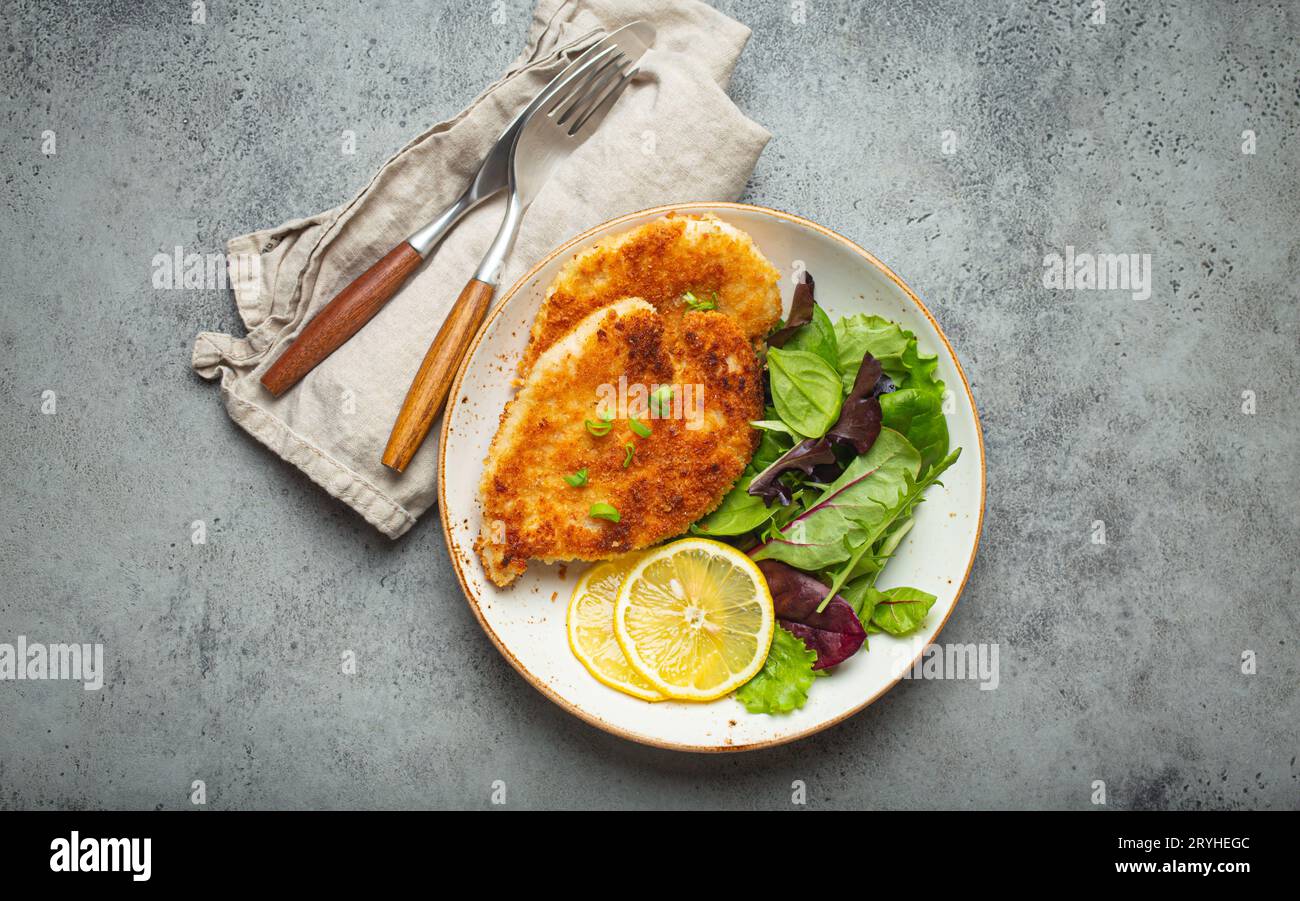 Crispy panko breaded fried chicken fillet with green salad and lemon on ...