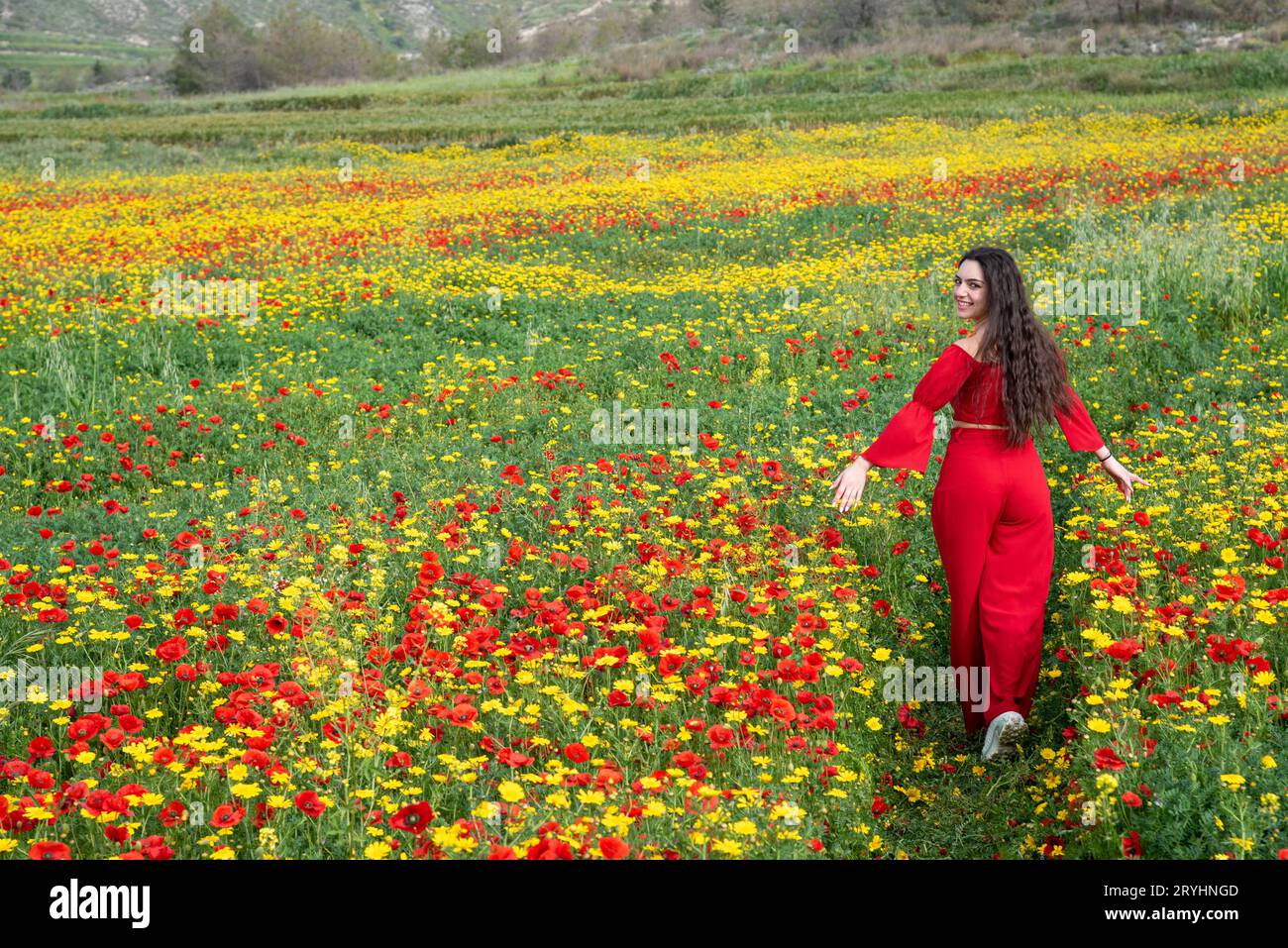 Attractive young woman wearing red dress walking happy in poppy flower ...