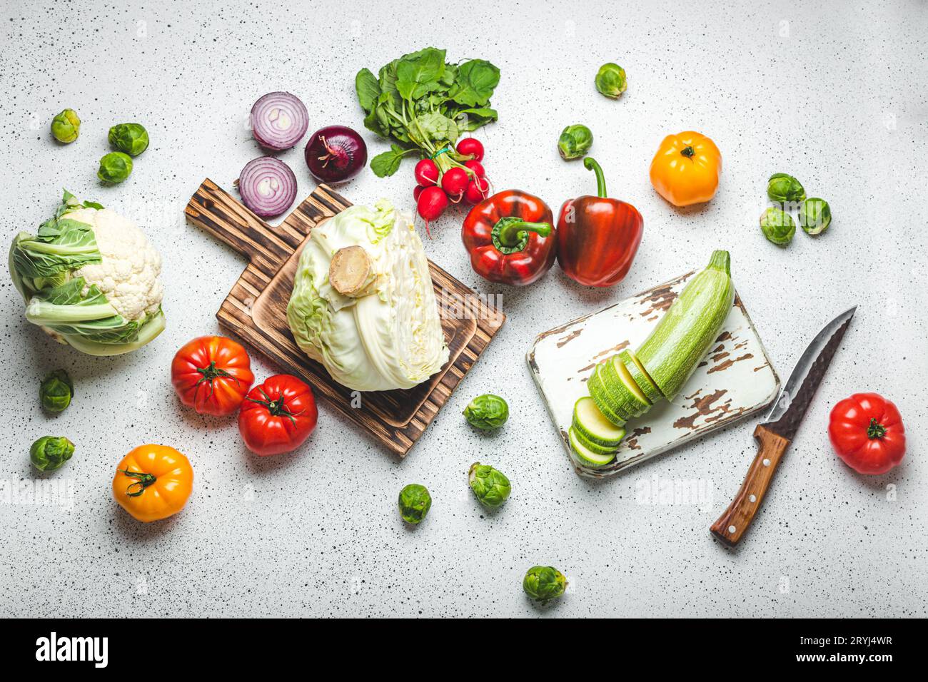 Fresh various vegetables with wooden cutting boards and knife on white kitchen table top view ...