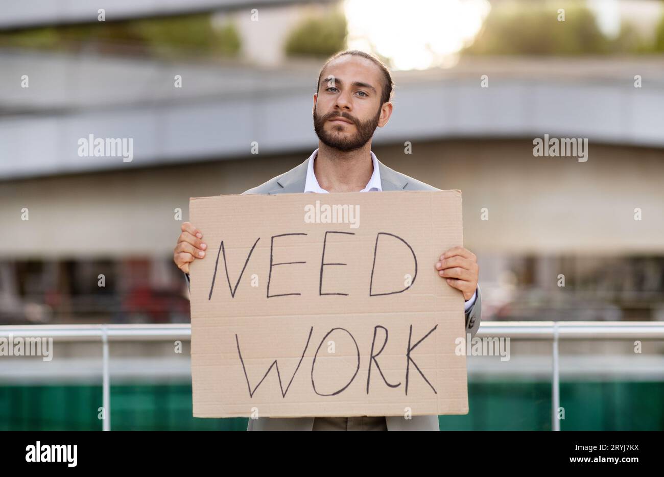Unemployed young man wearing suit standing on street, holding Need Work ...