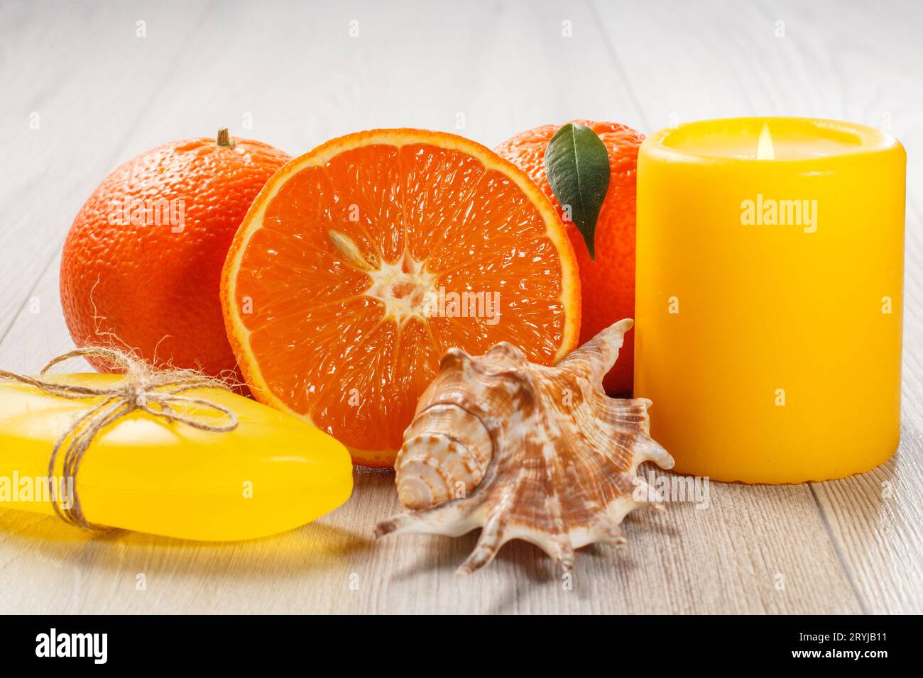 Cut orange with two whole oranges, soap, sea shell and burning candle ...