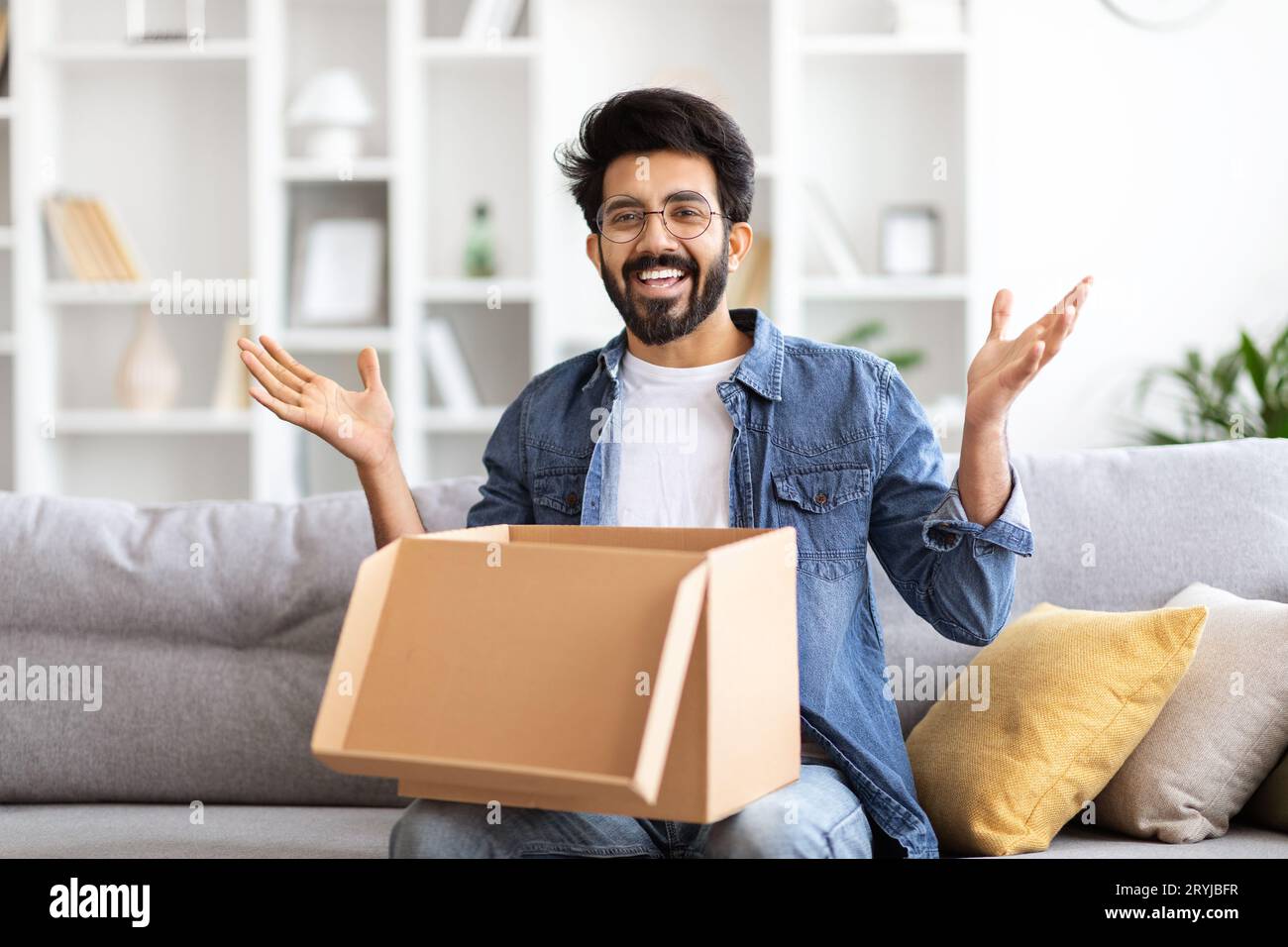 Excited indian man opening delivery box at home, raising hands with joy ...