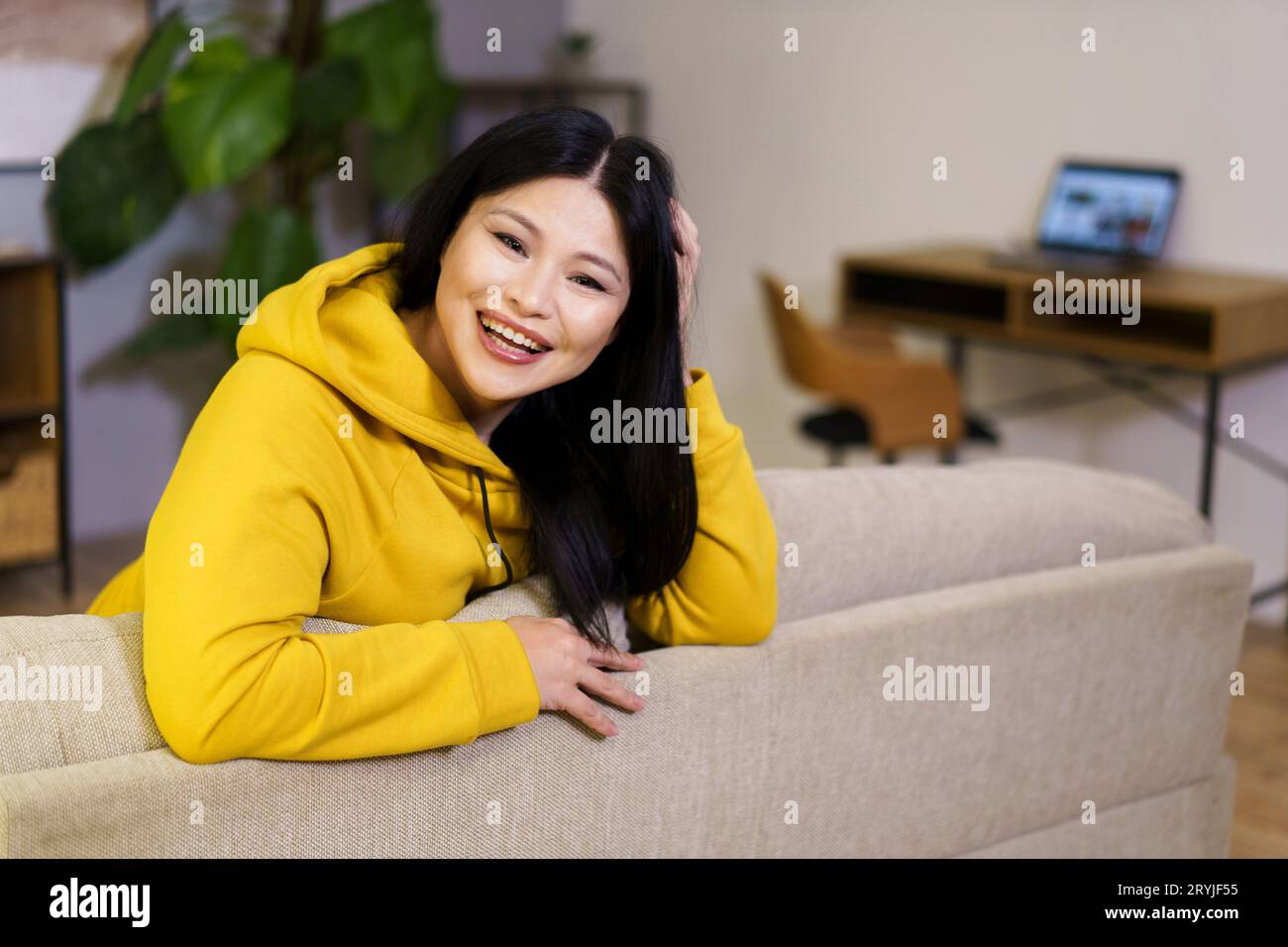 Beautiful middle-aged Asian woman is captured resting on a sofa in her ...