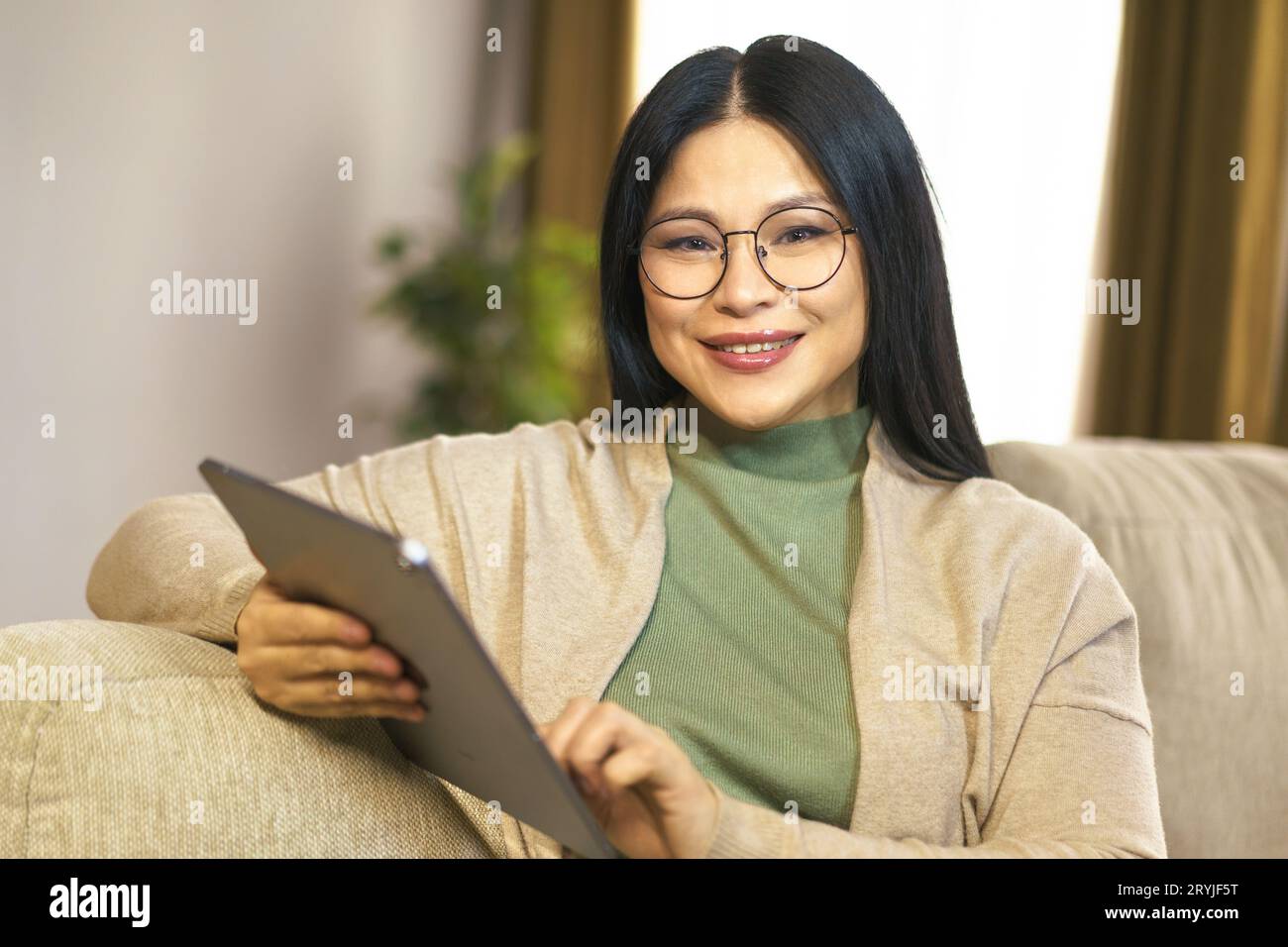 Confident middle-aged Asian woman enjoys moment of relaxation at home ...