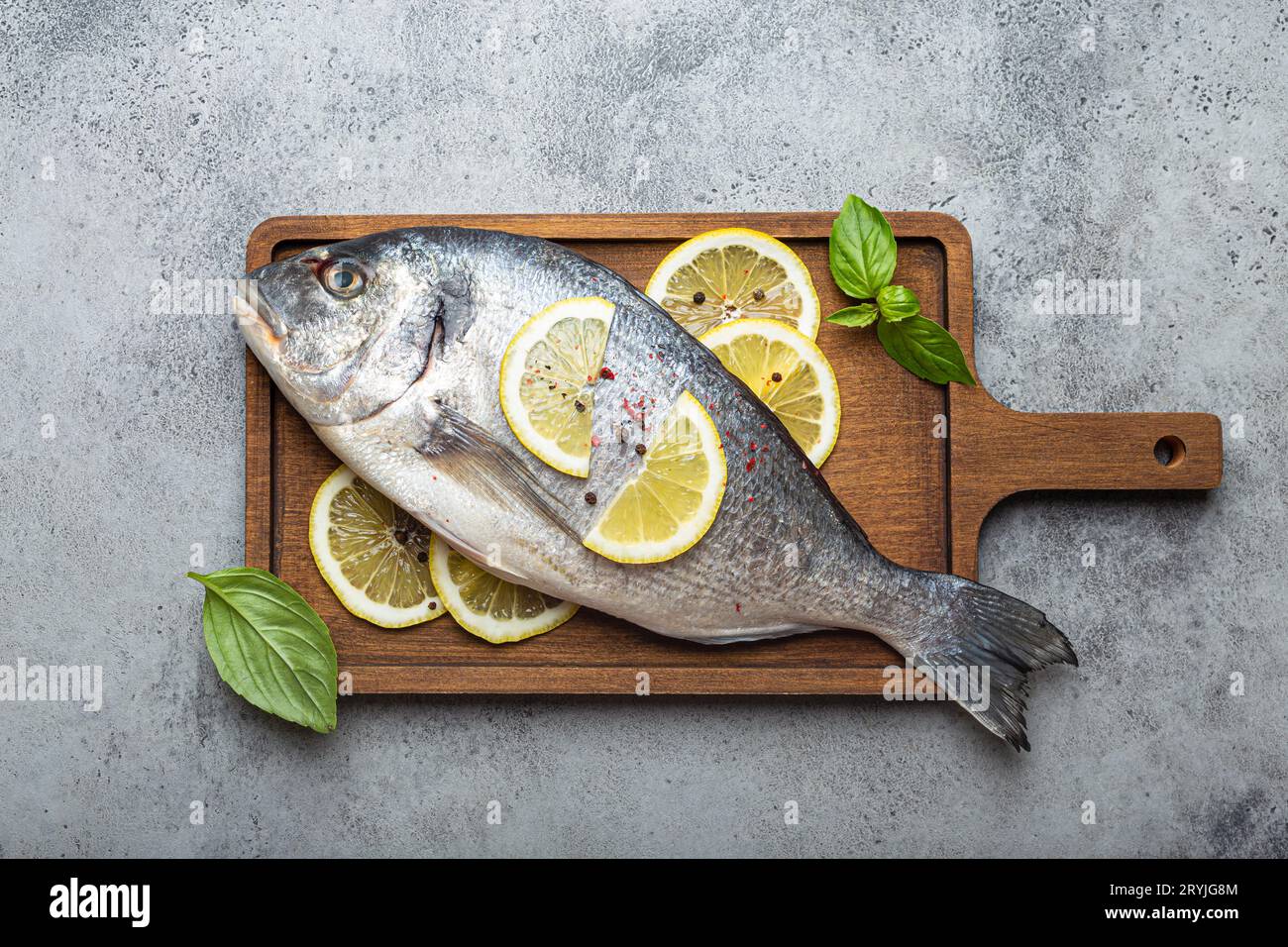 Raw uncooked fish dorado with lemon and fresh basil on wooden cutting ...