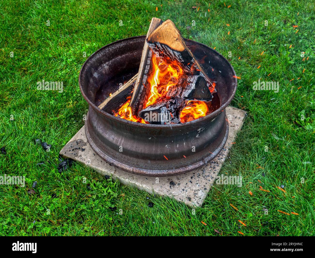 Campfire in a steel wheel on the concrete base and green lawn Stock ...