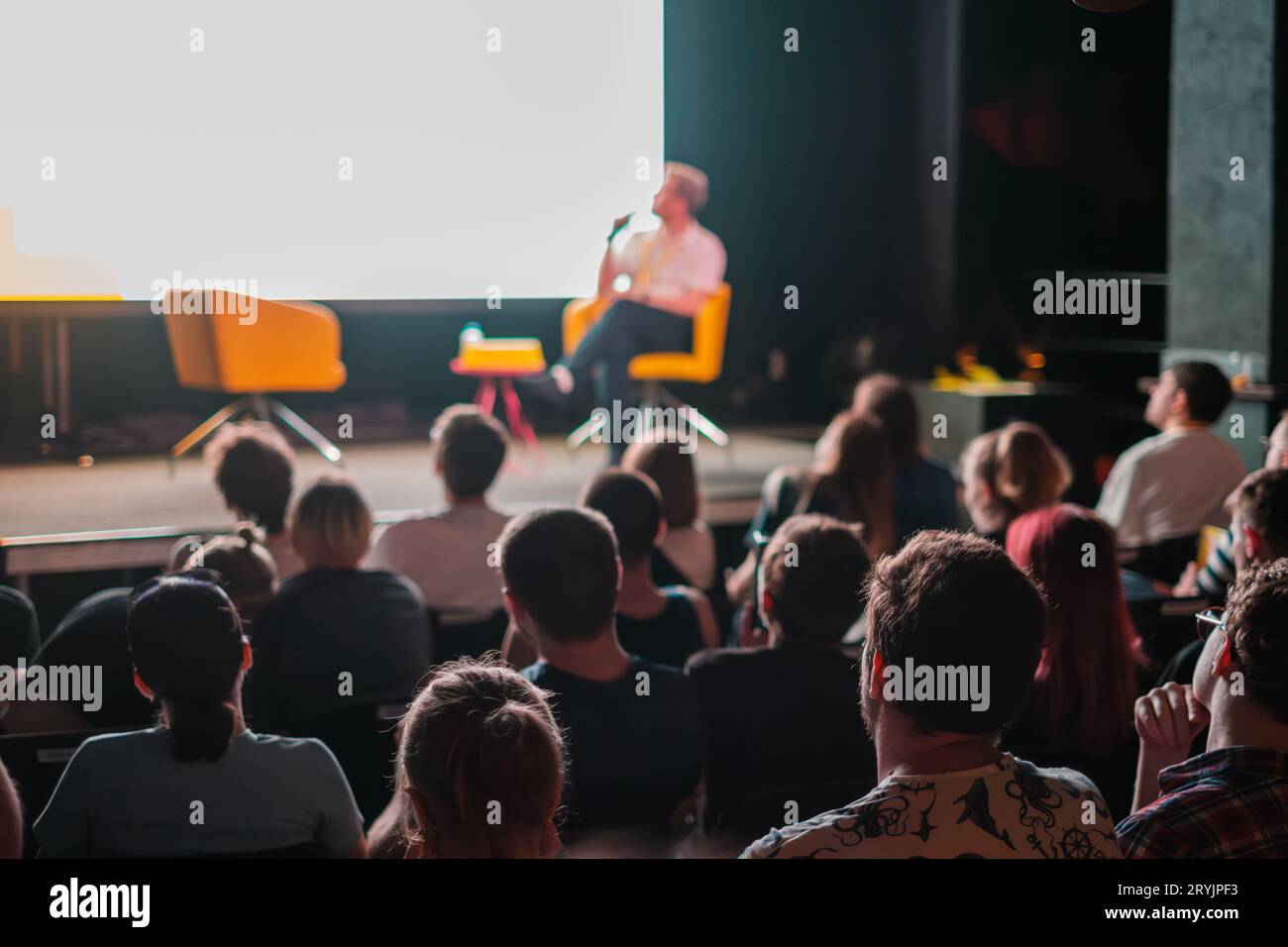 Crowd sitting in hall against blurred stage, while speaker showing ...