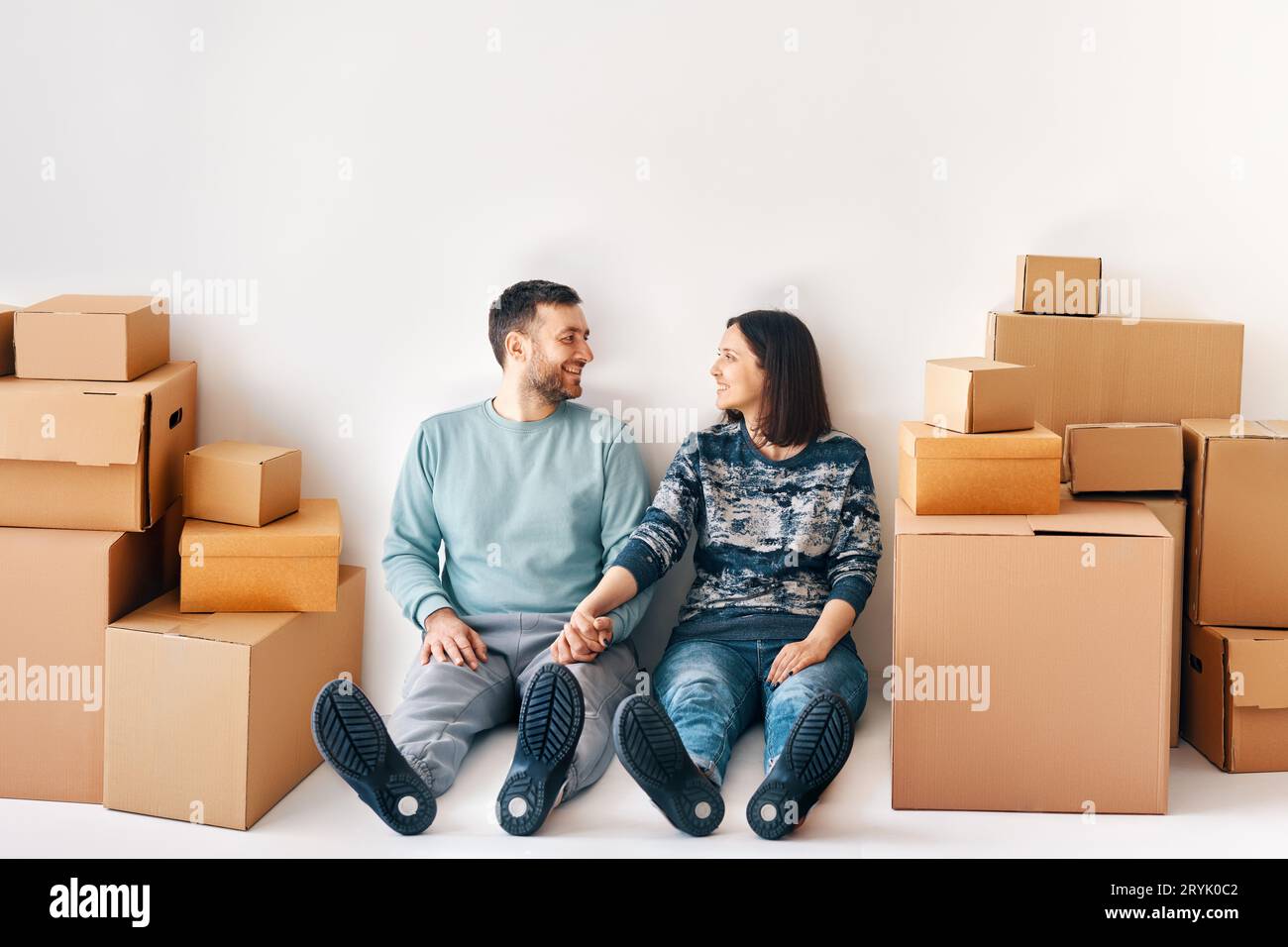 Happy smiling couple at new home sitting on floor surrounded by ...