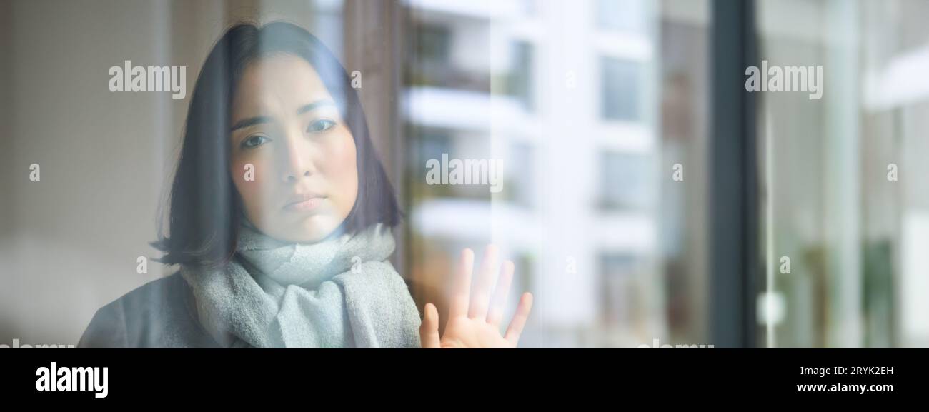 Asian woman feels unwell, stays at home, looks outside window with ...