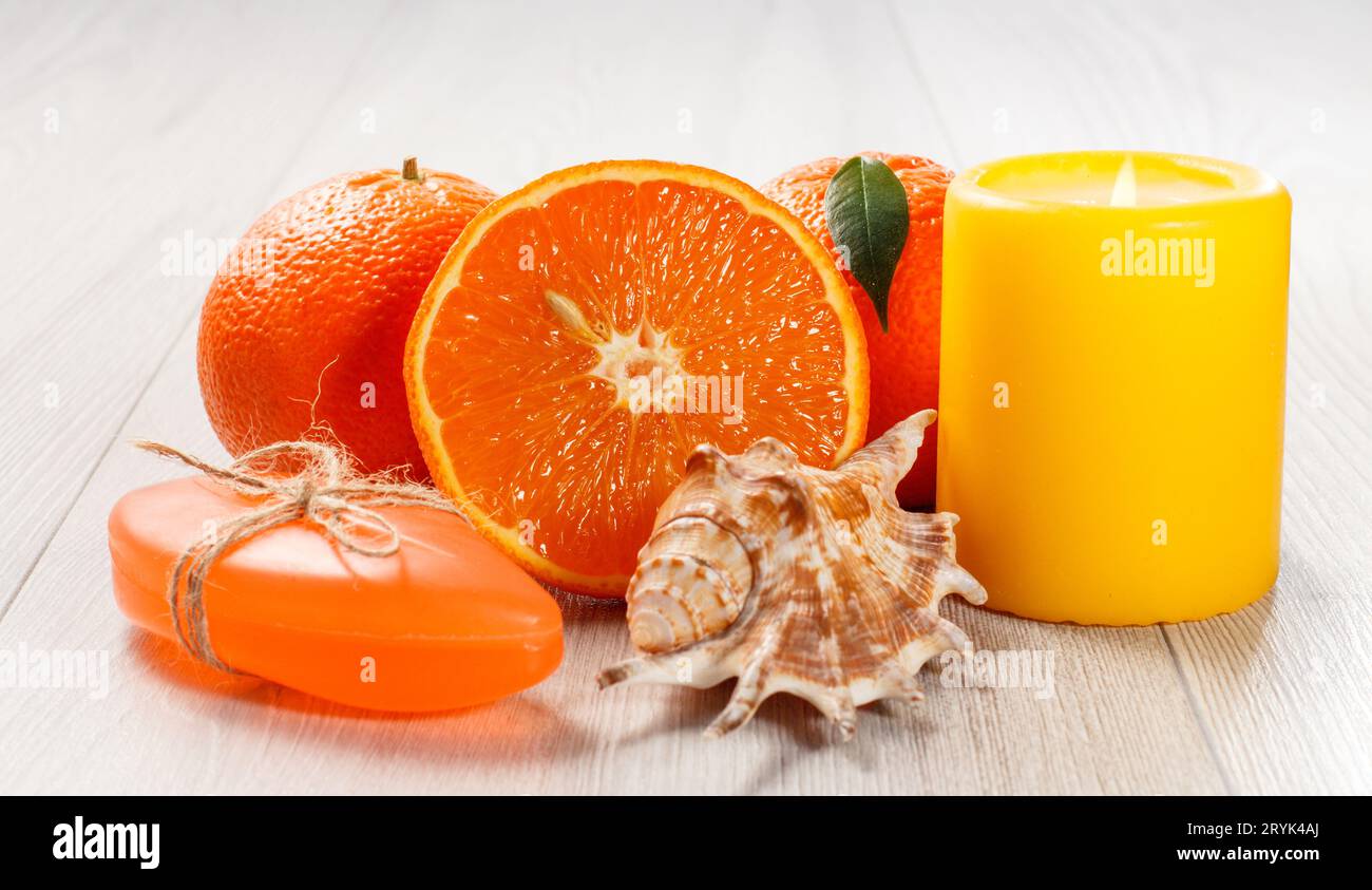 Cut orange with two whole oranges, soap, sea shell and burning candle ...