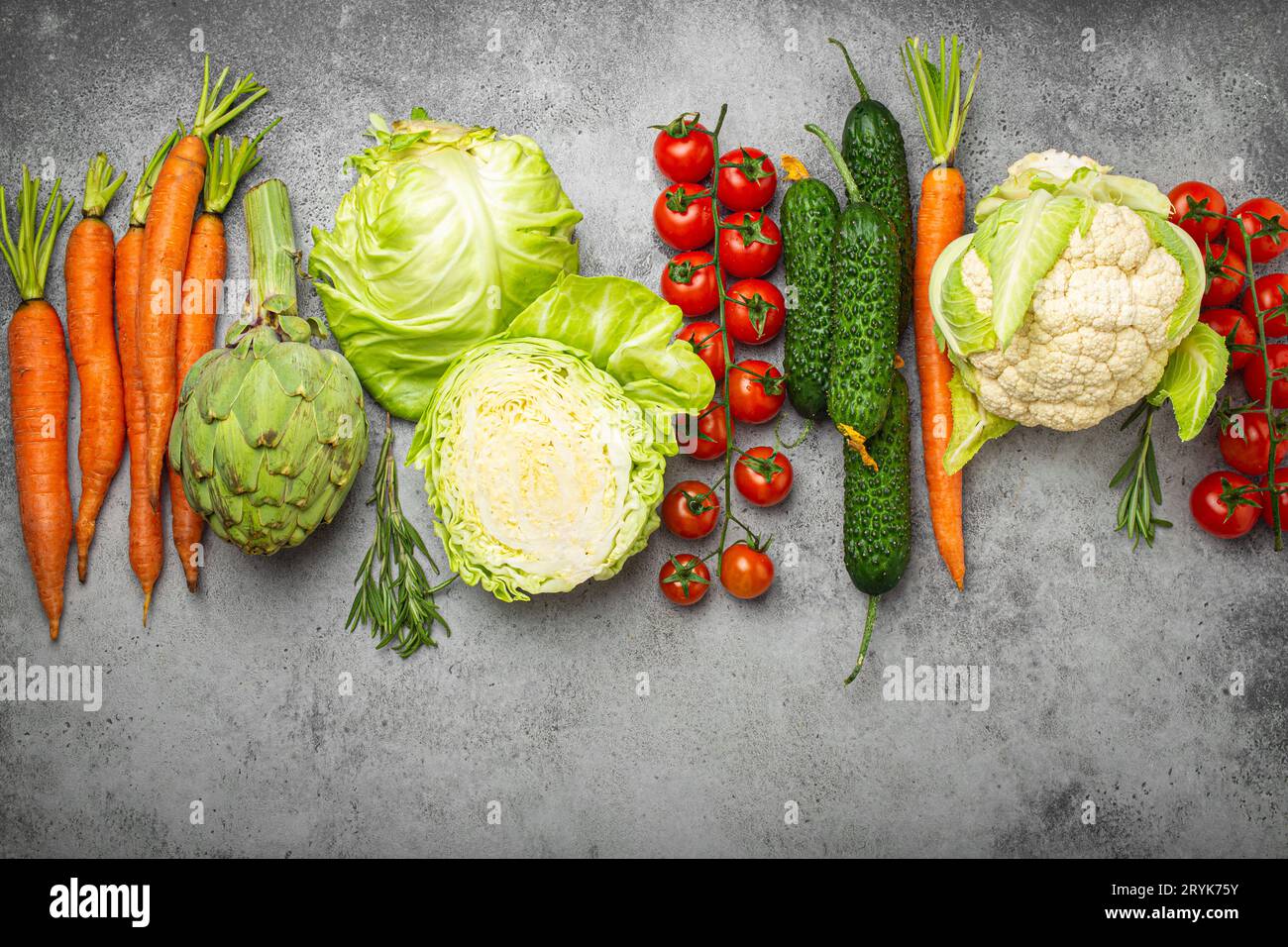 Fresh assorted organic vegetables arranged in line on rustic grey stone ...