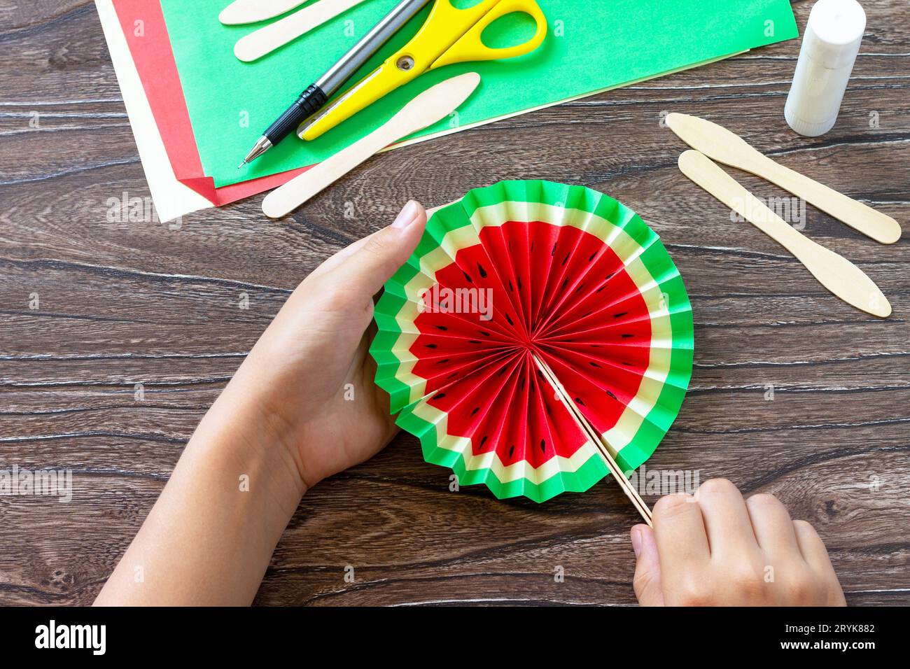In the hands of a child Paper Fan watermelon on a wooden table ...