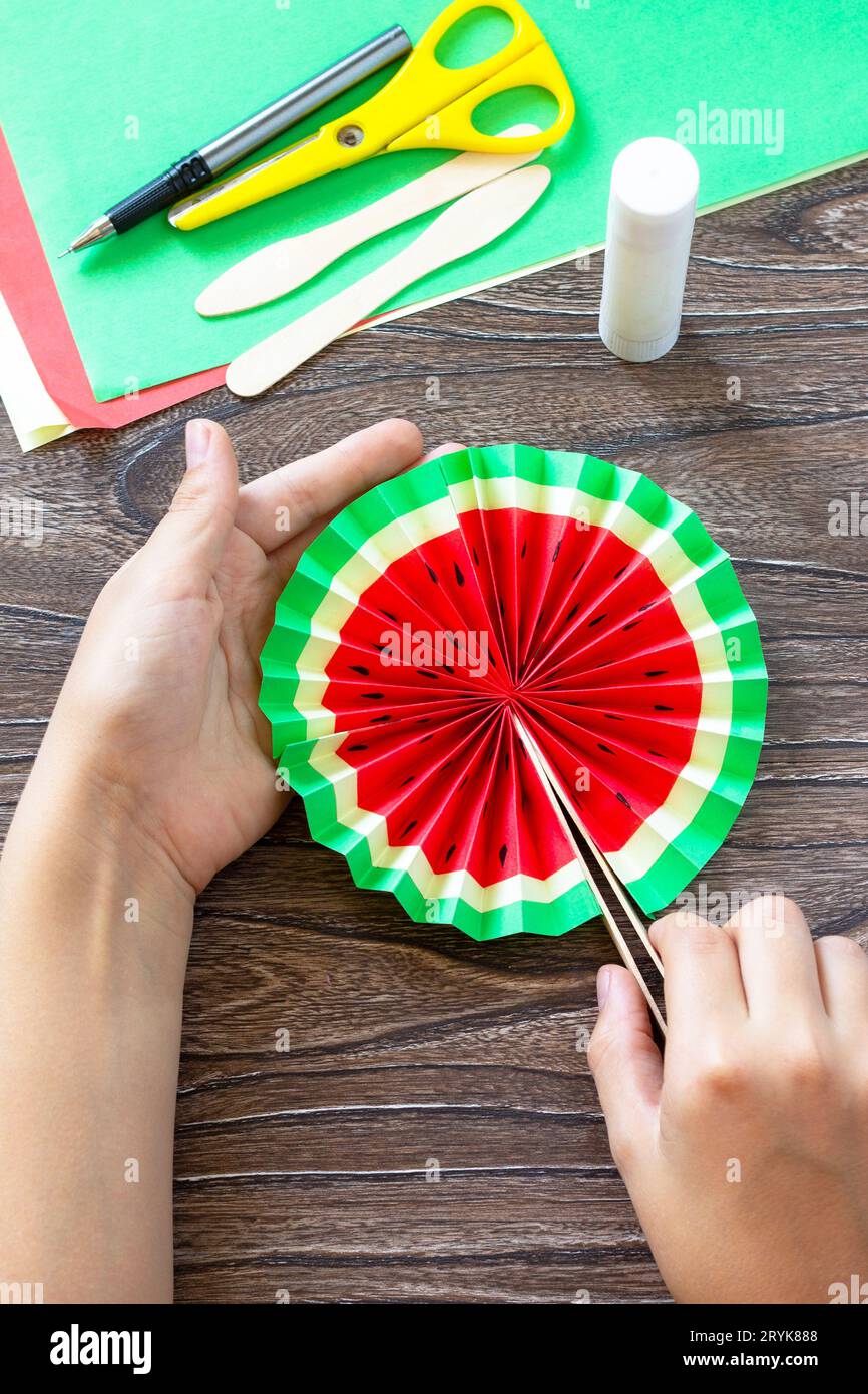 In the hands of a child Paper Fan watermelon on a wooden table ...