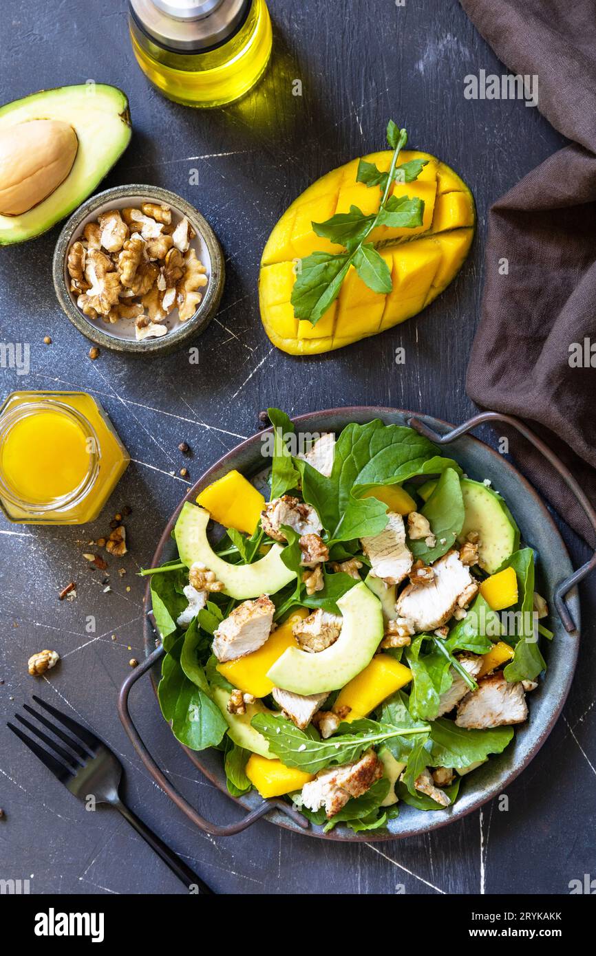 Healthy diet salad with arugula, mango, avocado, chicken grill, walnuts and vinaigrette dressing ...