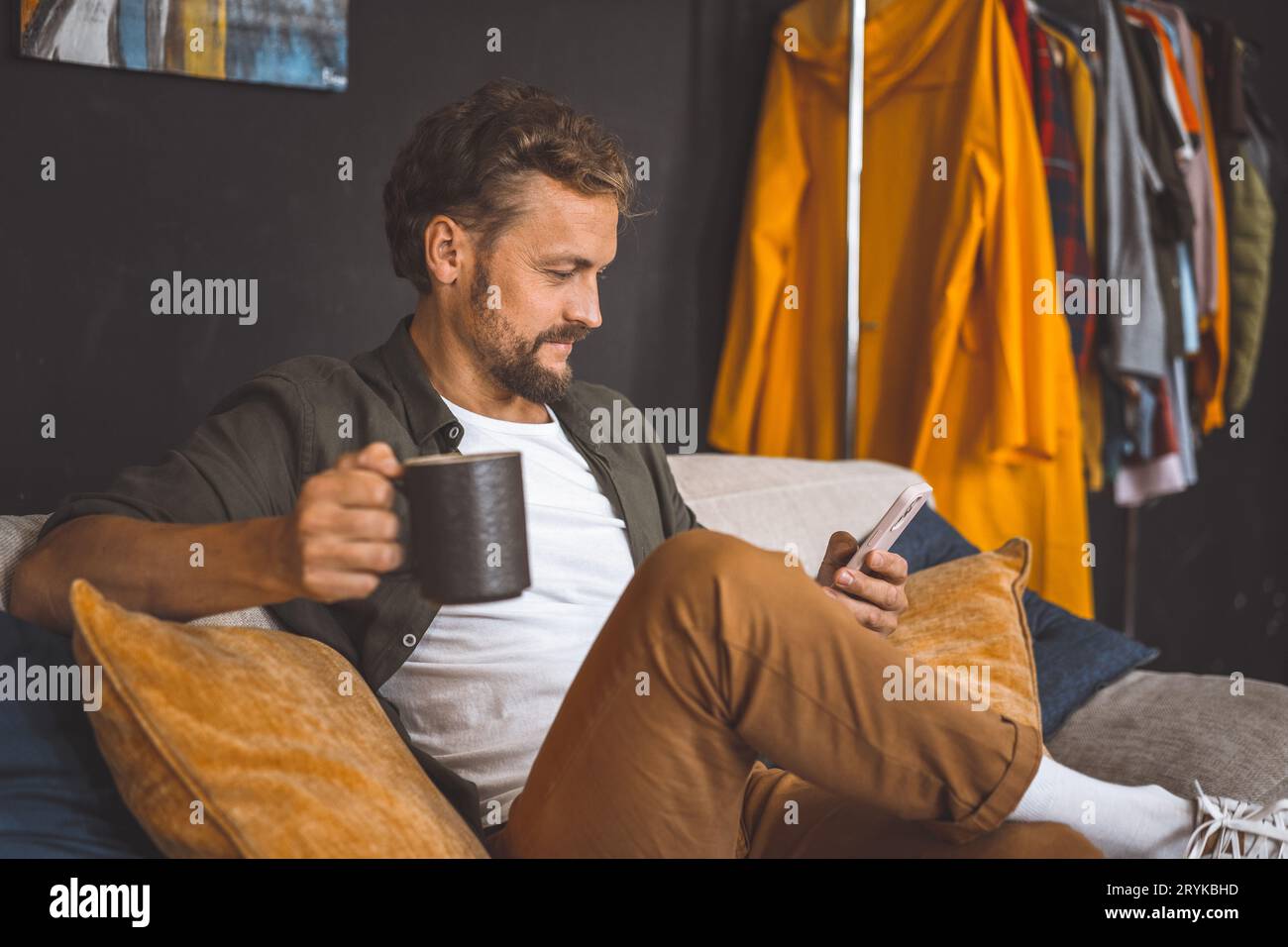 Man taking break at home, enjoying cup of coffee while focused on phone ...