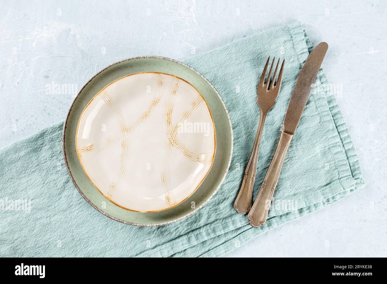 An empty plate with a gold rim, with a fork and a knife, with a teal ...