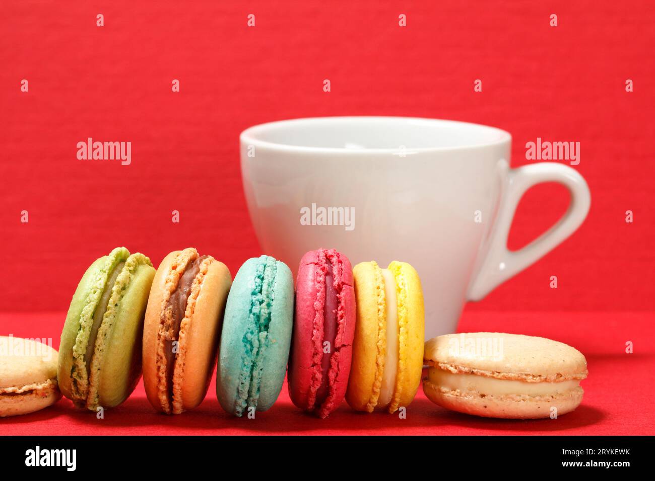 Sweet macarons cakes of different colors with a cup on the red textured ...
