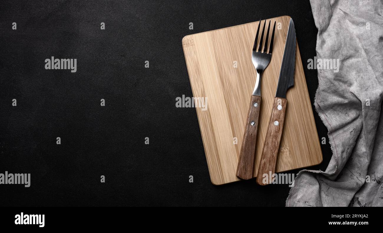 Fork and knife with wooden handle and cutting board on black background ...