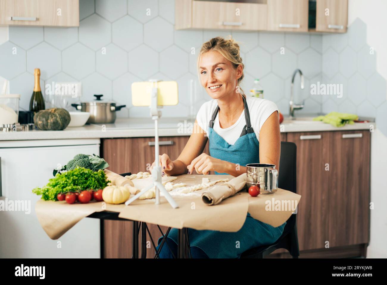 A young woman prepares at the table in the kitchen with a video recipe ...
