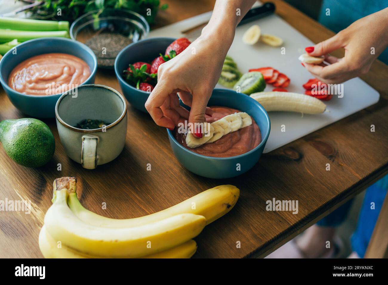 Female hands lay out sliced fruits on a bowl with pink chia pudding ...