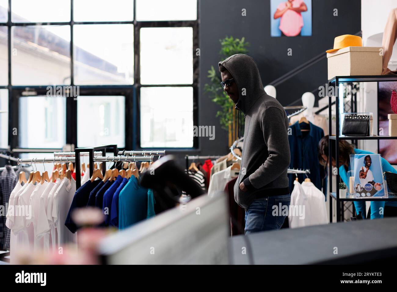 African american man wearing hood and glasses trying to steal fashionable clothes from modern ...