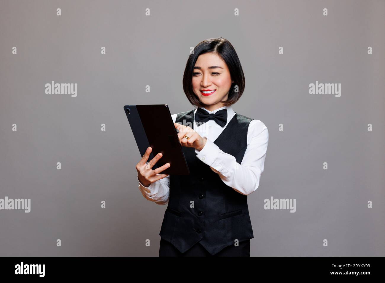 Smiling restaurant receptionist in uniform checking guest list on ...