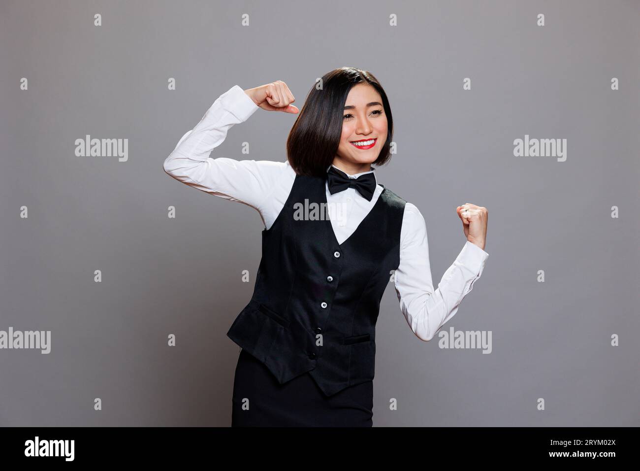 Smiling cheerful attractive asian waitress laughing while showing bicep ...