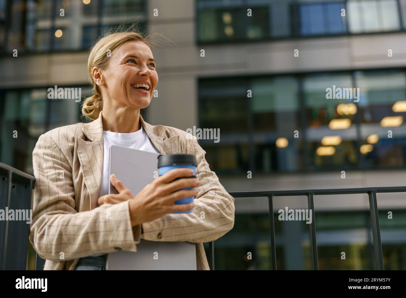 Woman freelancer standing with laptop and coffee cup on modern building ...