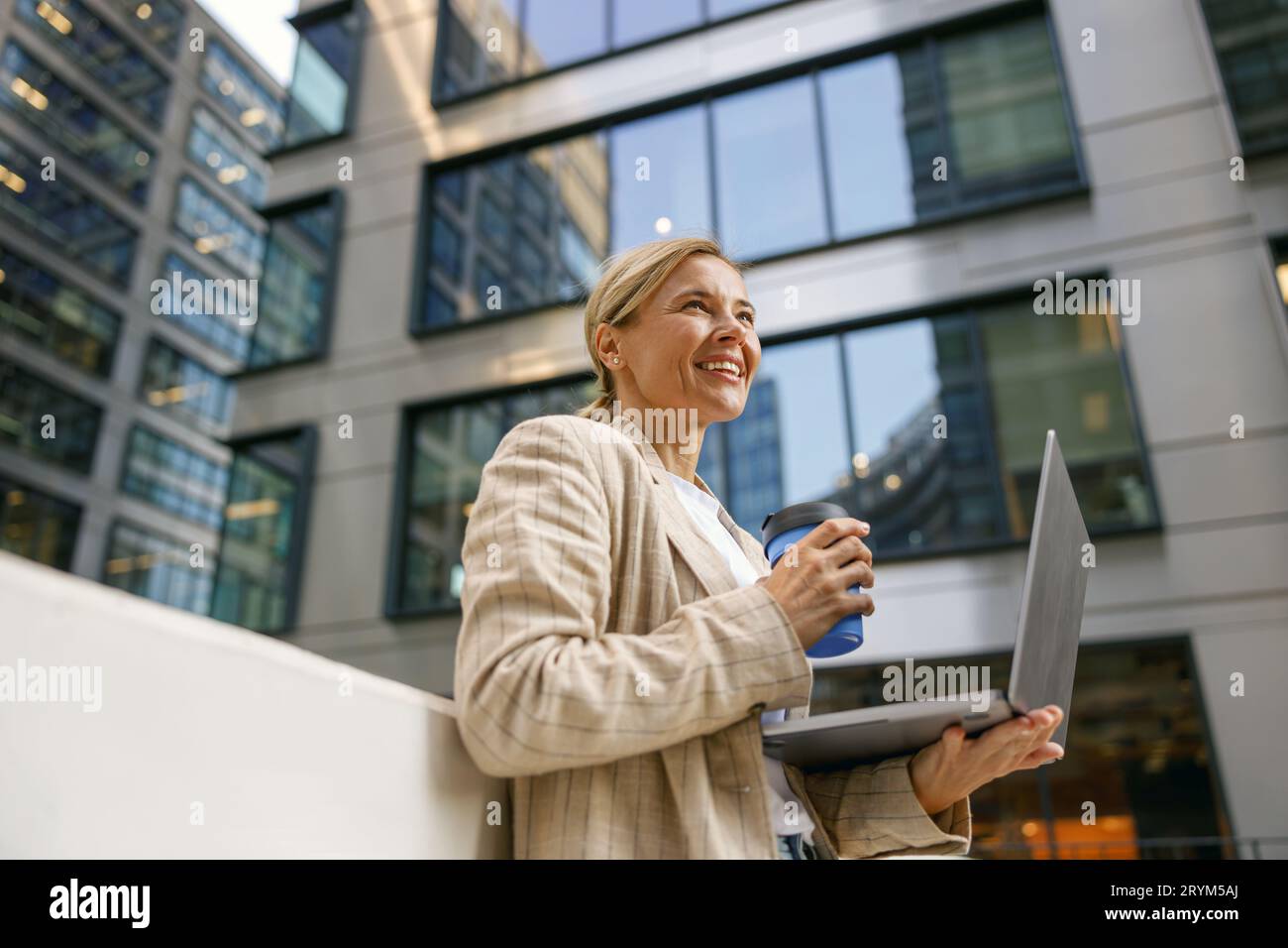 Woman manager drinking coffee while working laptop on modern building ...