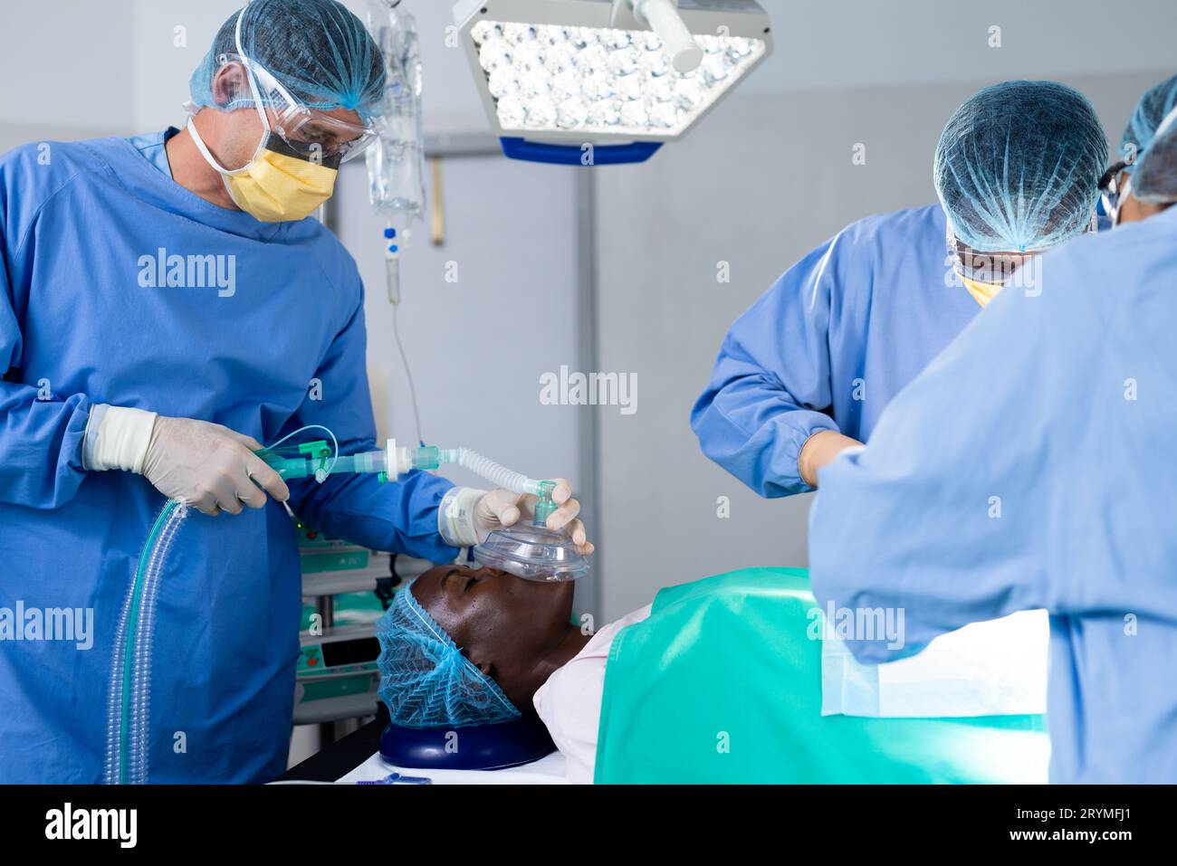 Diverse group of surgeons with male patient being given anesthetic mask ...